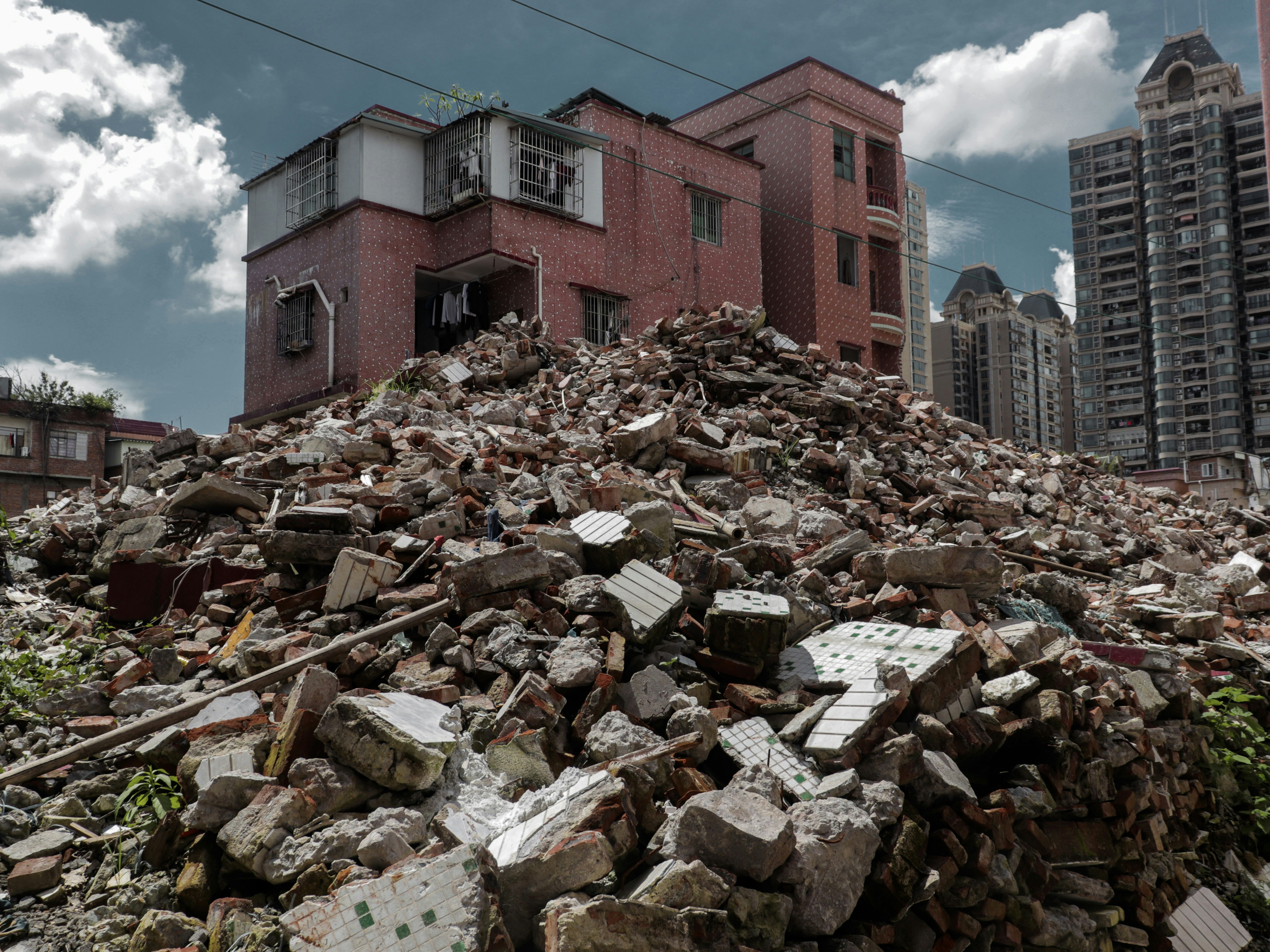 Rubble Summit: A Red Brick House Framed by Distant Skyscrapers