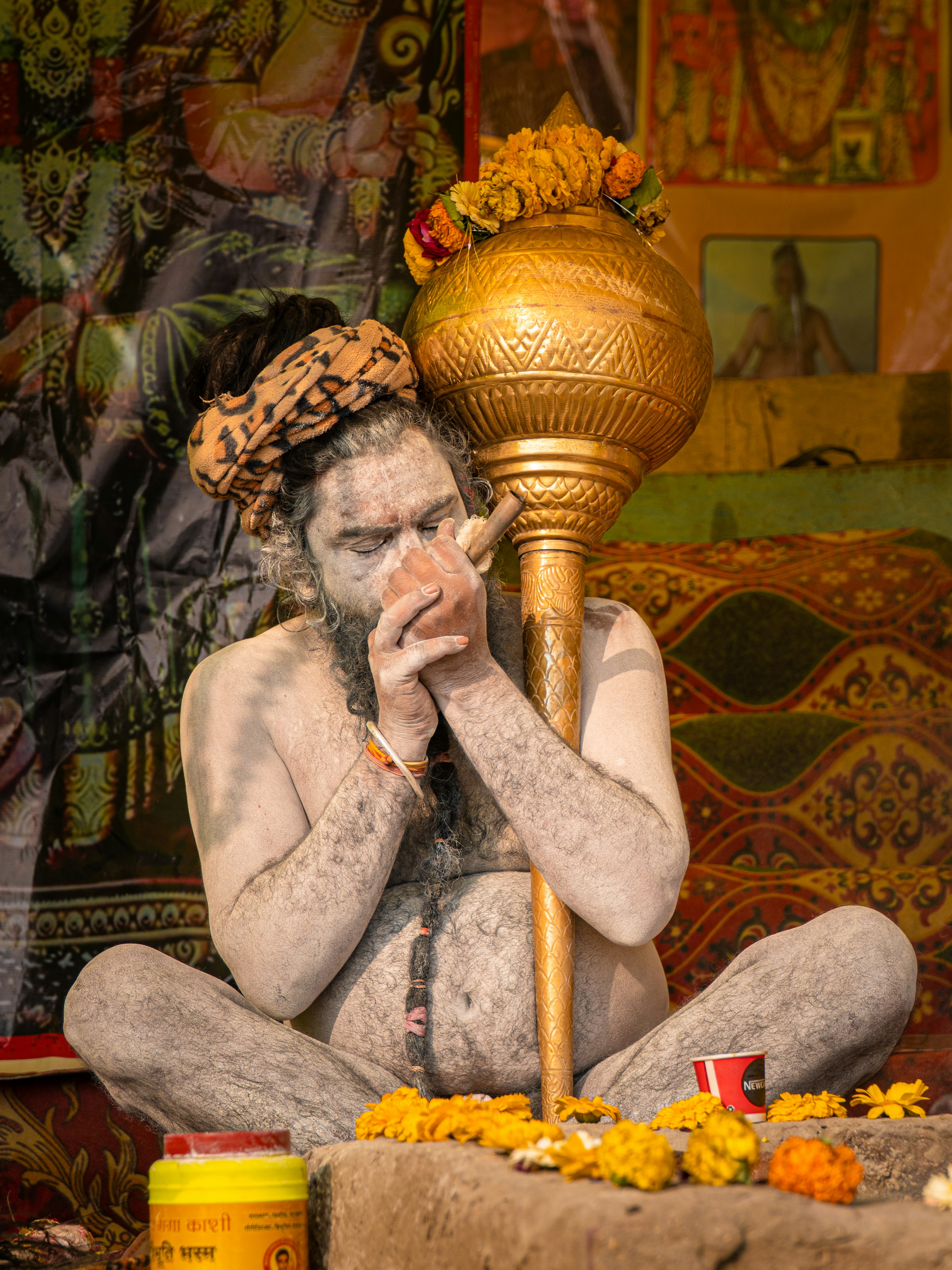 Sadhu covered in ash, using a chillum, and posing with a large symbolic mace.