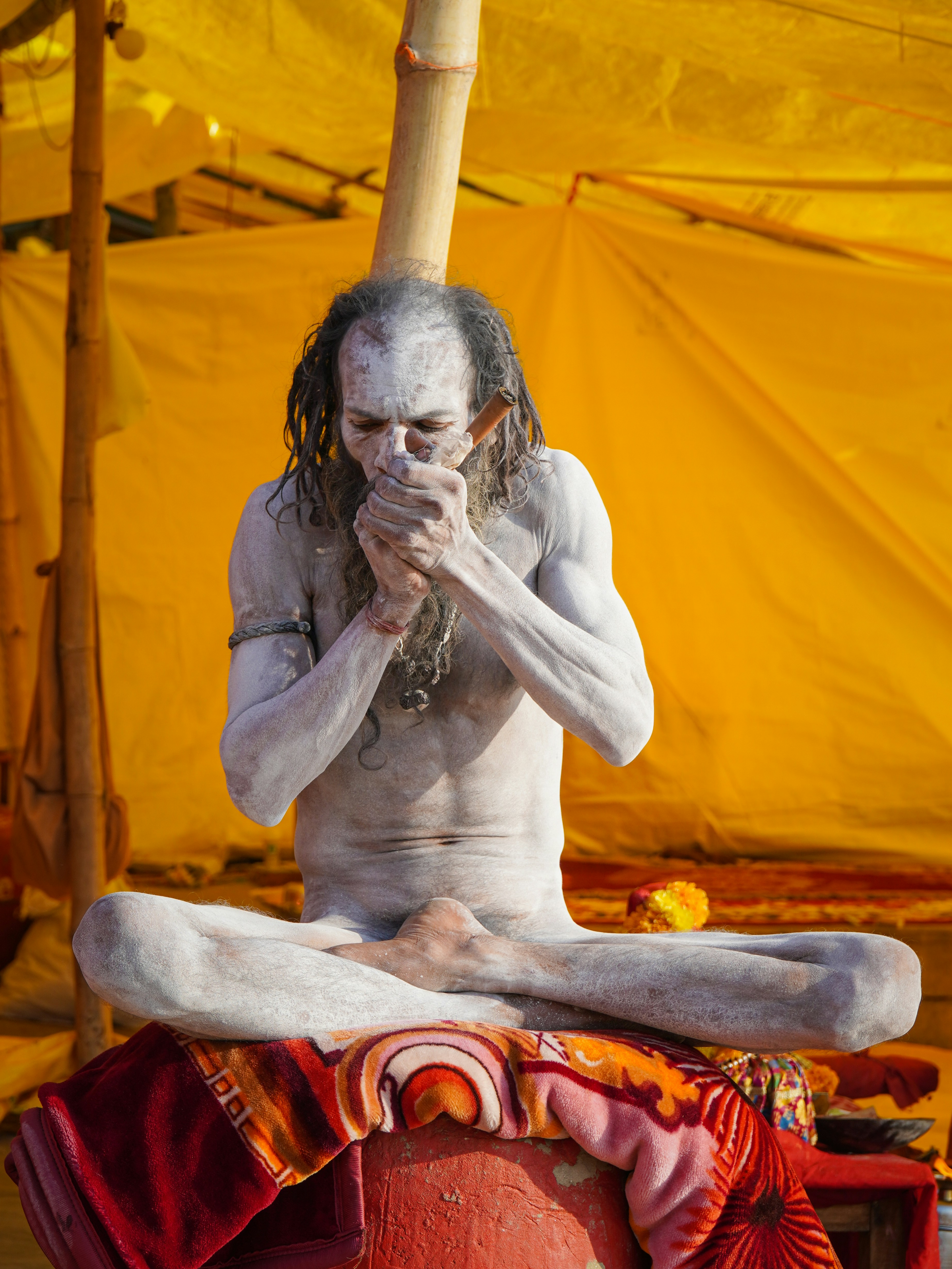 Meditative White Body Painted Seated in Bright Yellow Camp Under a Canopy