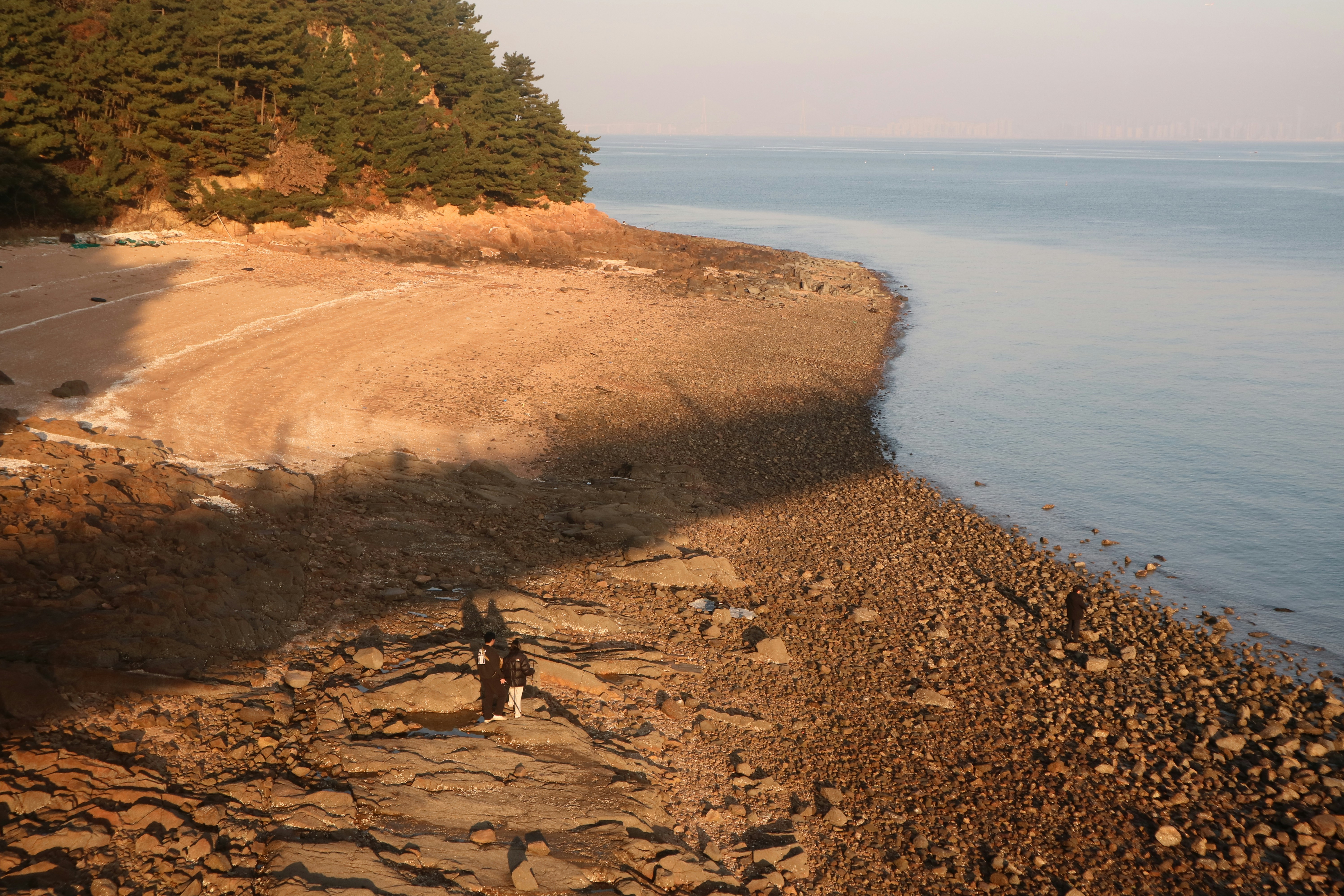 Sunlit Reach: A lone figure tracing the rocky shoreline at dusk