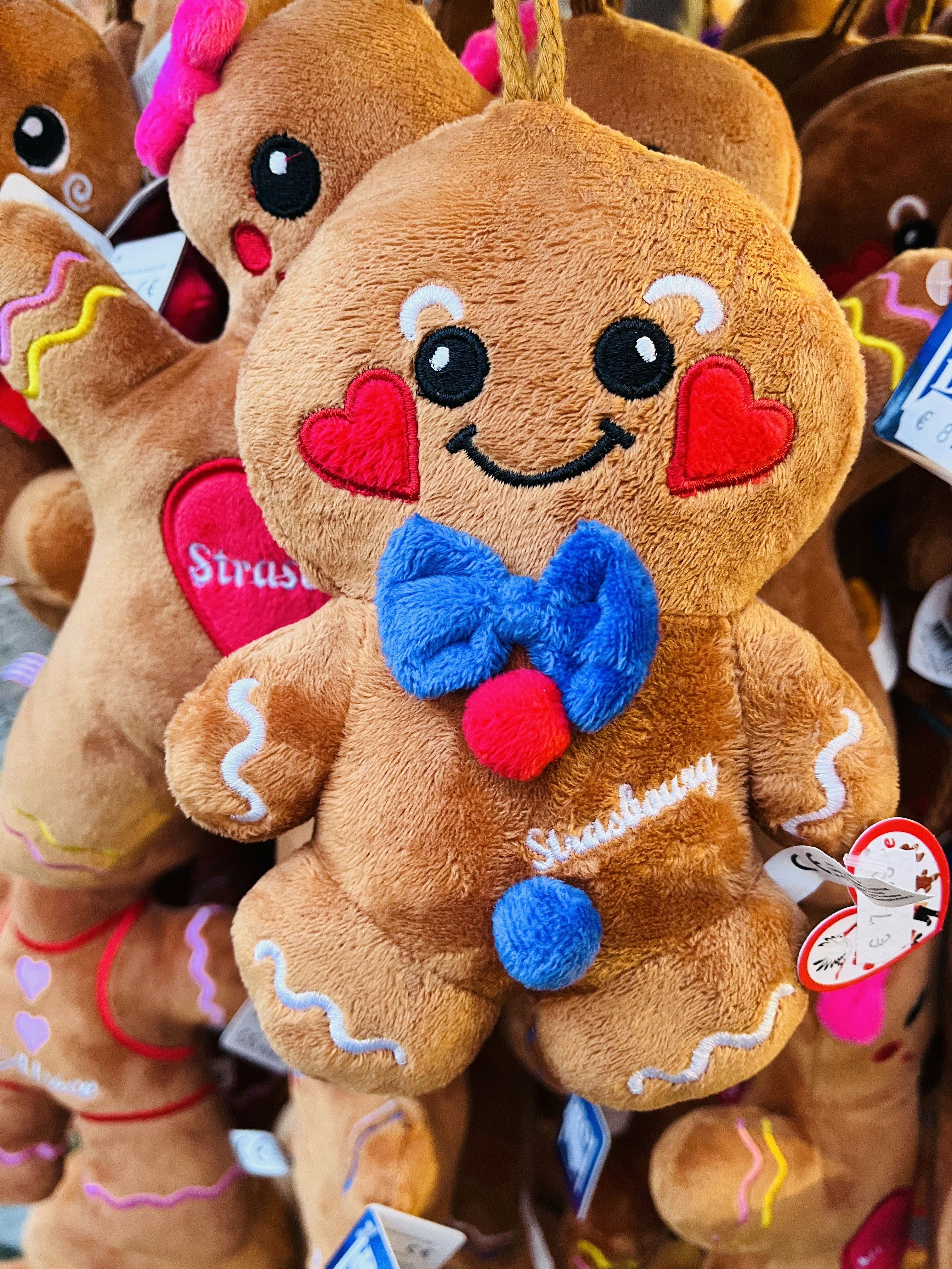 Gingerbread Plush with Heart Cheeks and Blue Bow in a Colorful Toy Display