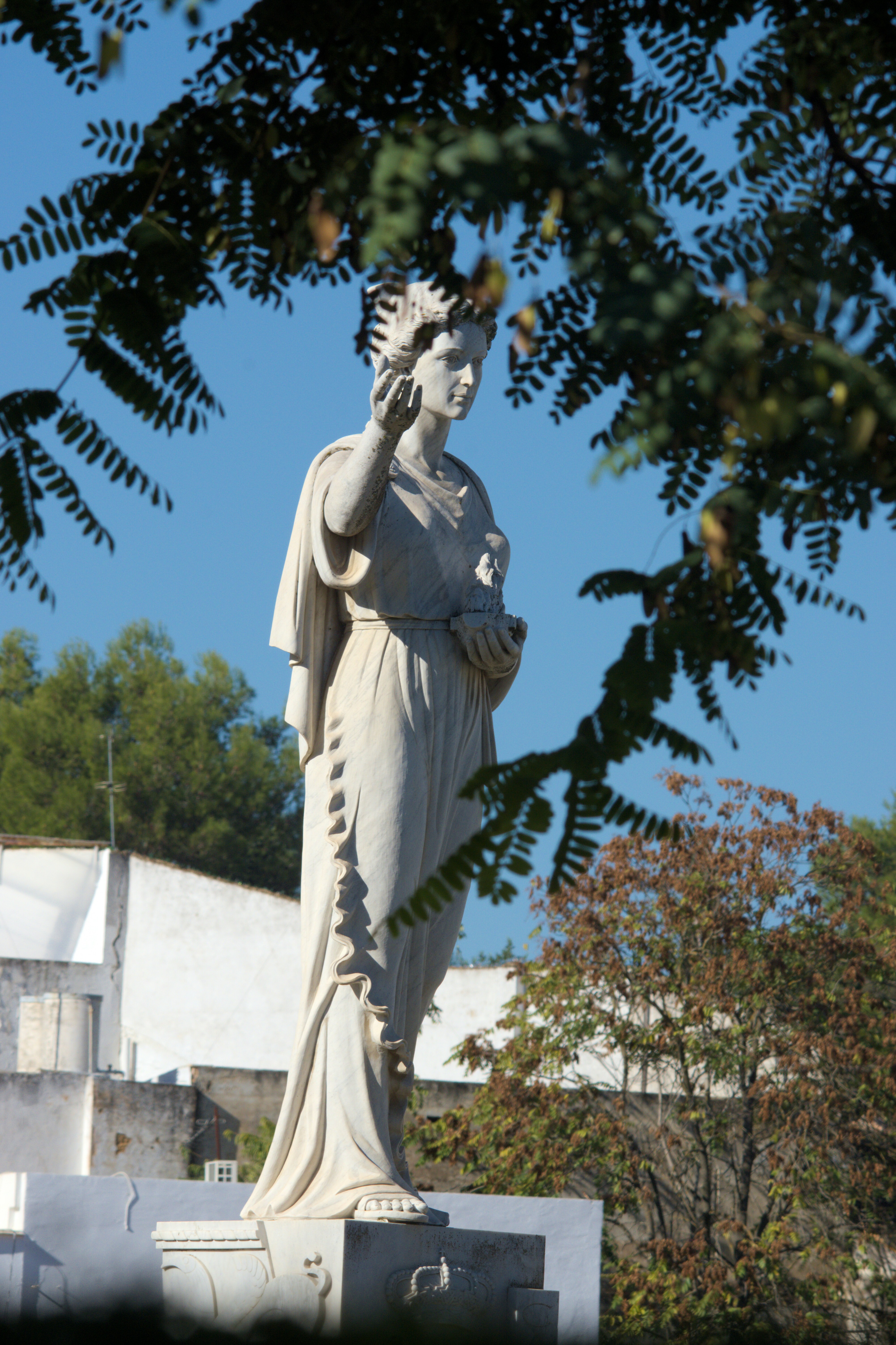 Sentinel of Marble: Sunlit Statue Framed by Foliage