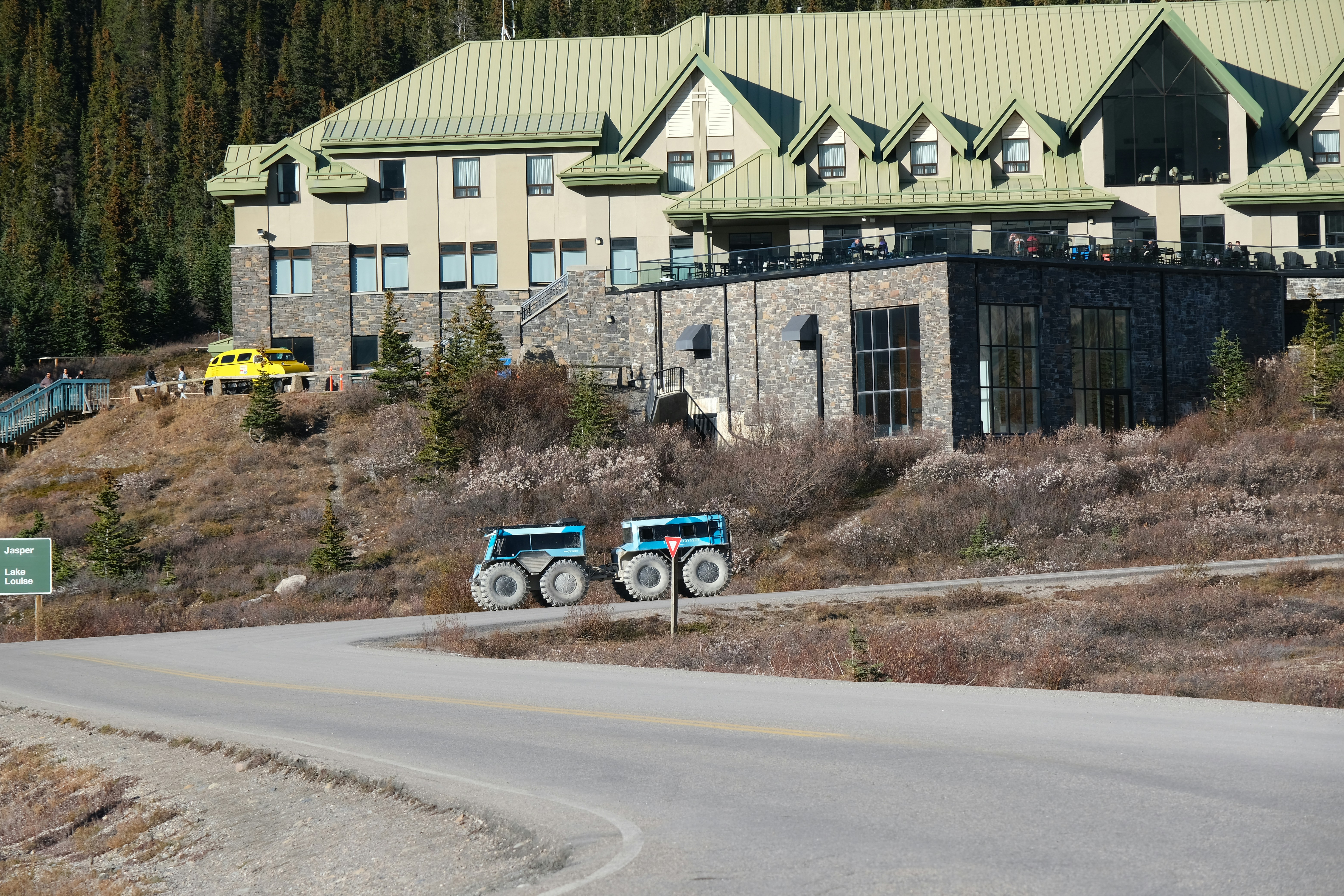 Blue Dump Trucks on a Winding Road Before a Green-Roofed Lodge