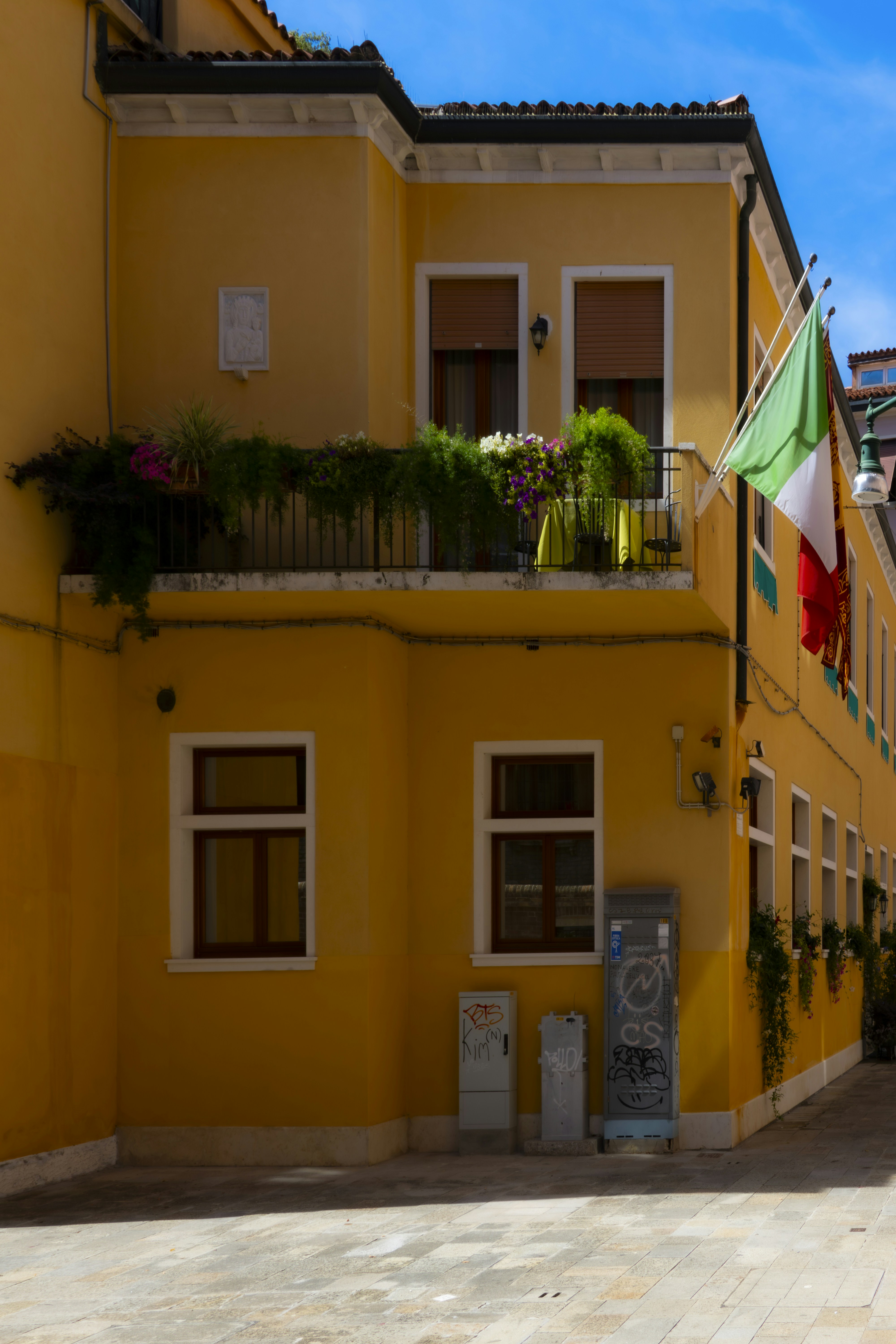 Sunlit Balcony Bloom: Italian Flag Framing a Yellow Courtyard
