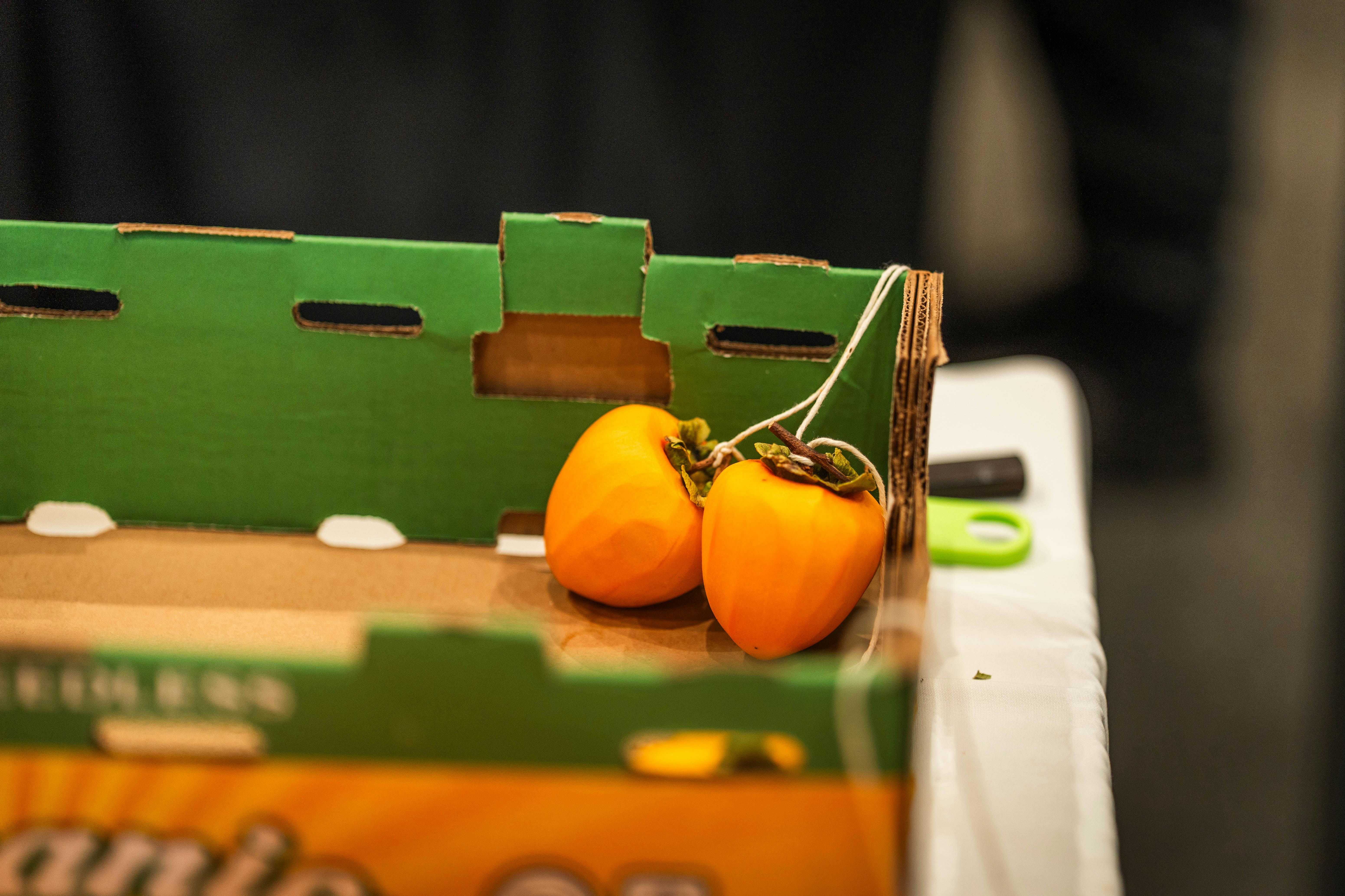 Two Persimmons in a Green Crate: Quiet Still-Life on a White Table