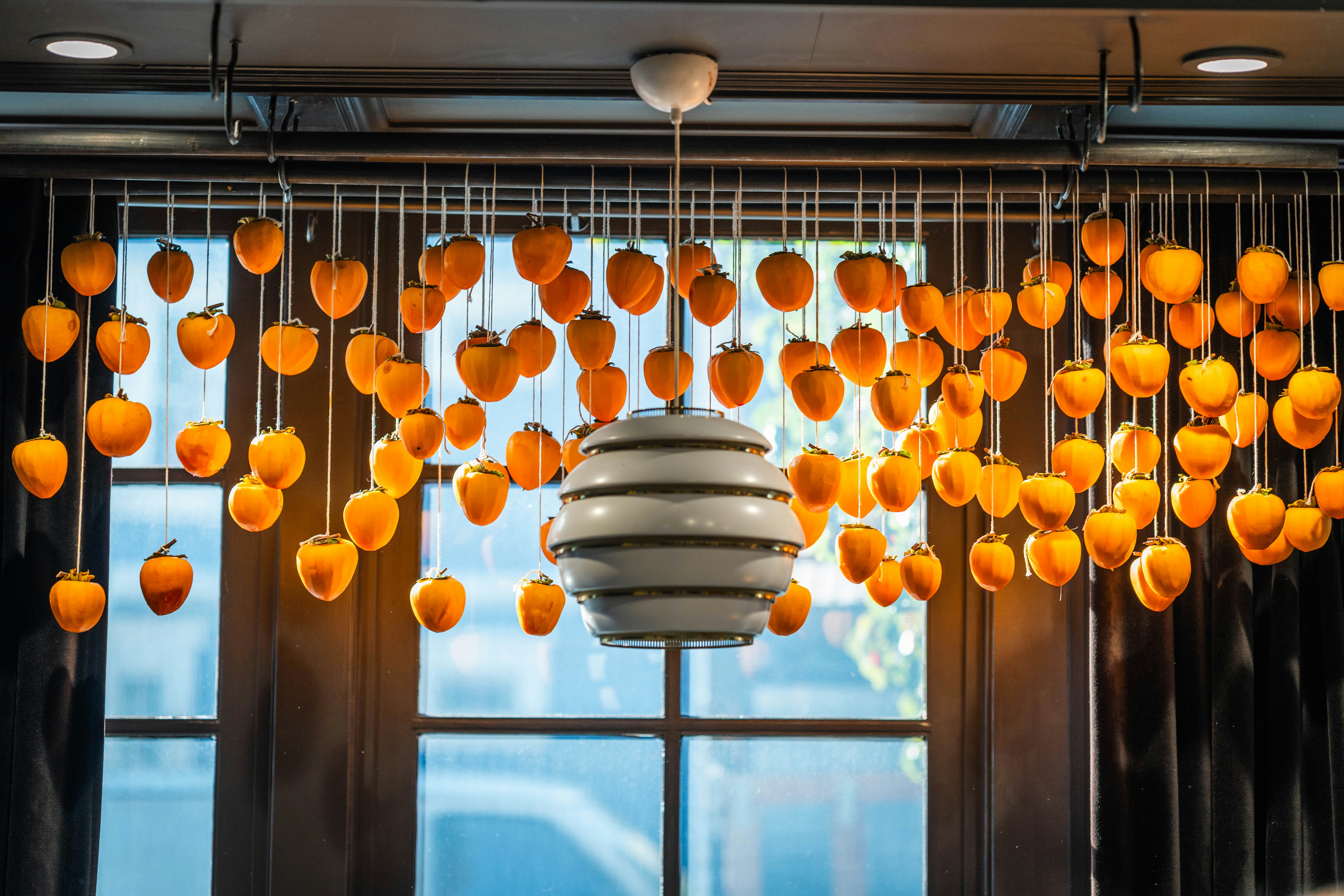 Oranges on Strings: A Warm-Window Still Life with a Striped Pendant Light