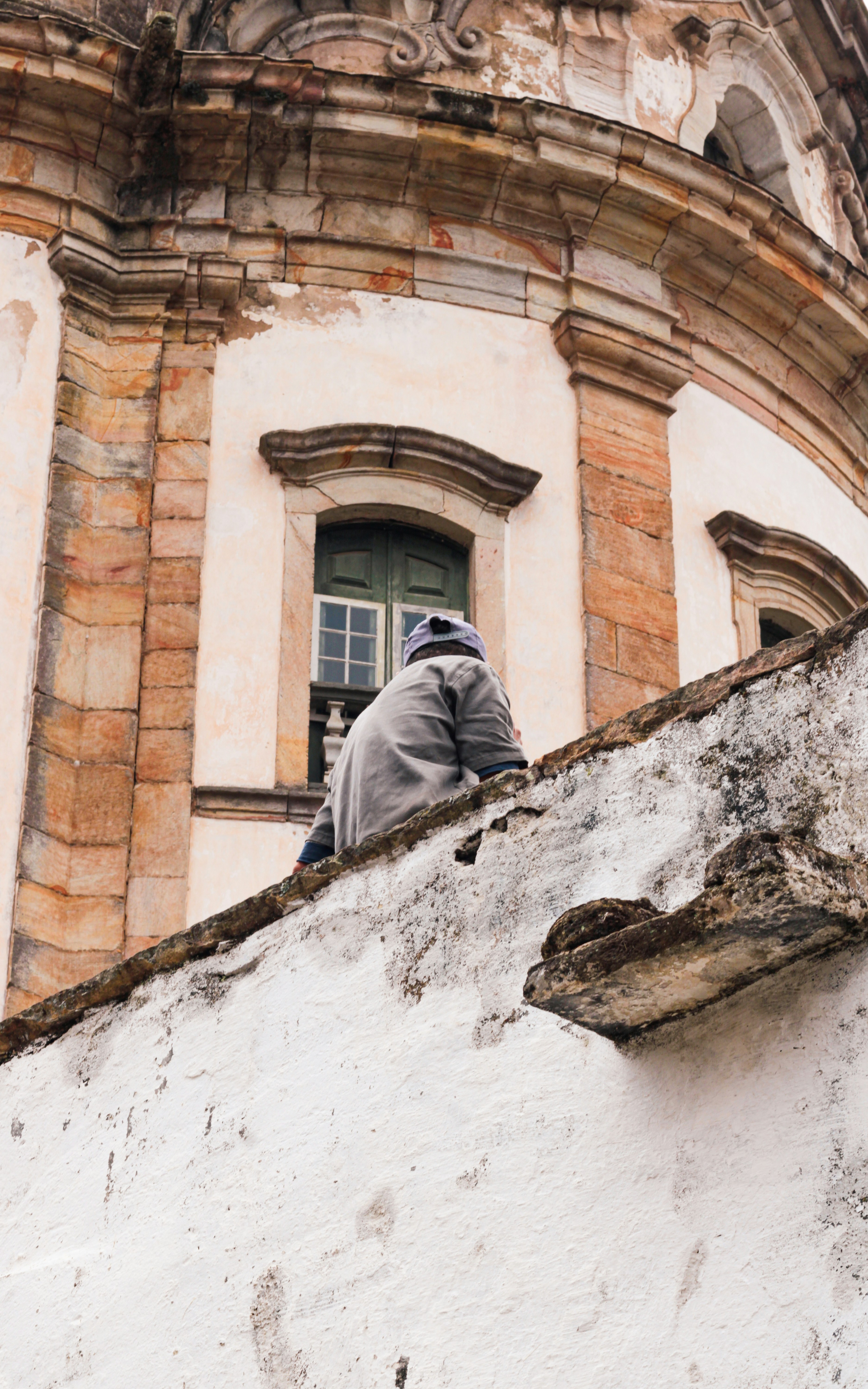 Lone Hooded Figure on a Weathered Terrace Before a Baroque Brick Facade