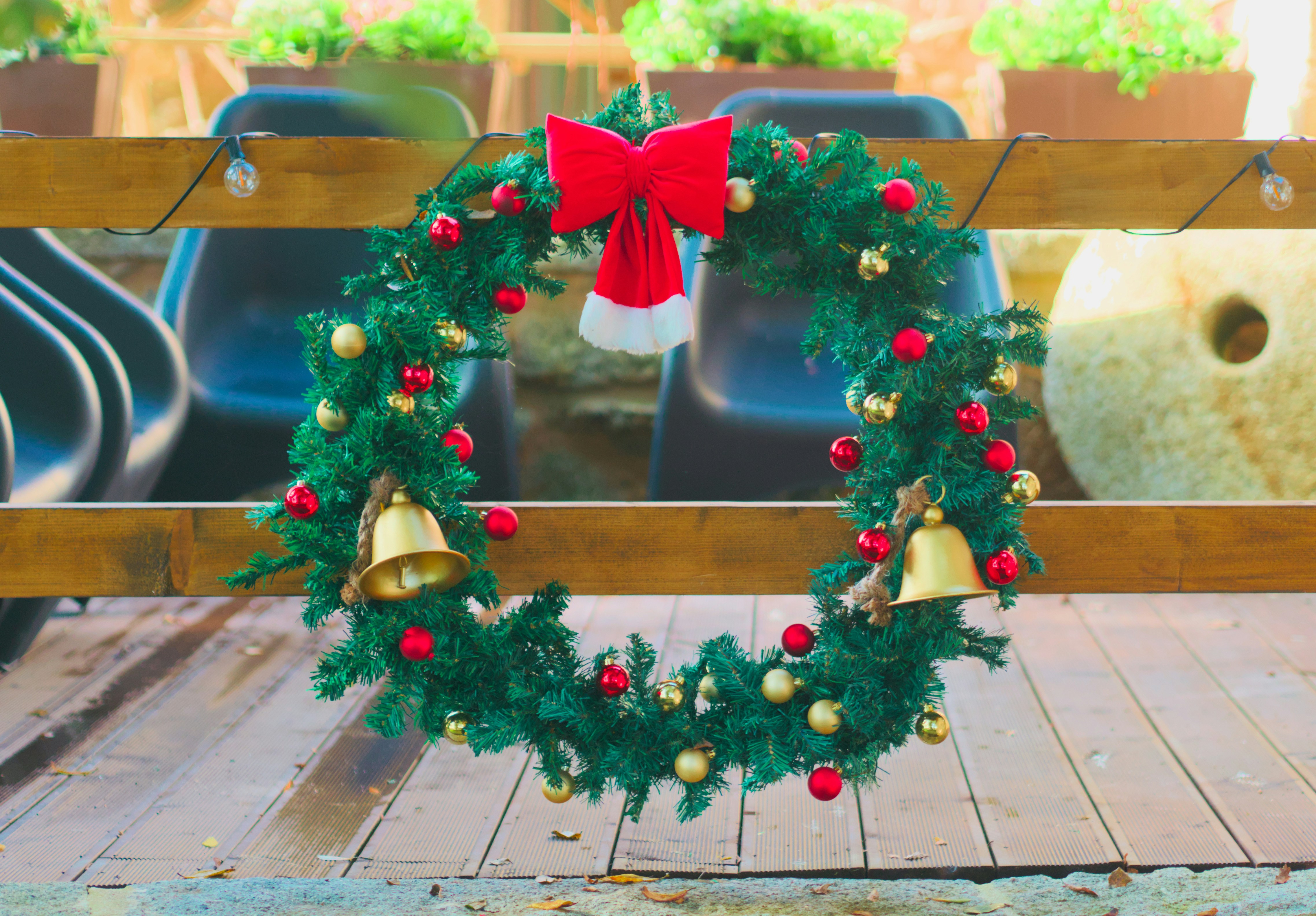 Sunlit Wreath on a Wooden Railing: Festive Red Bow and Golden Bells Framing Holiday Cheer