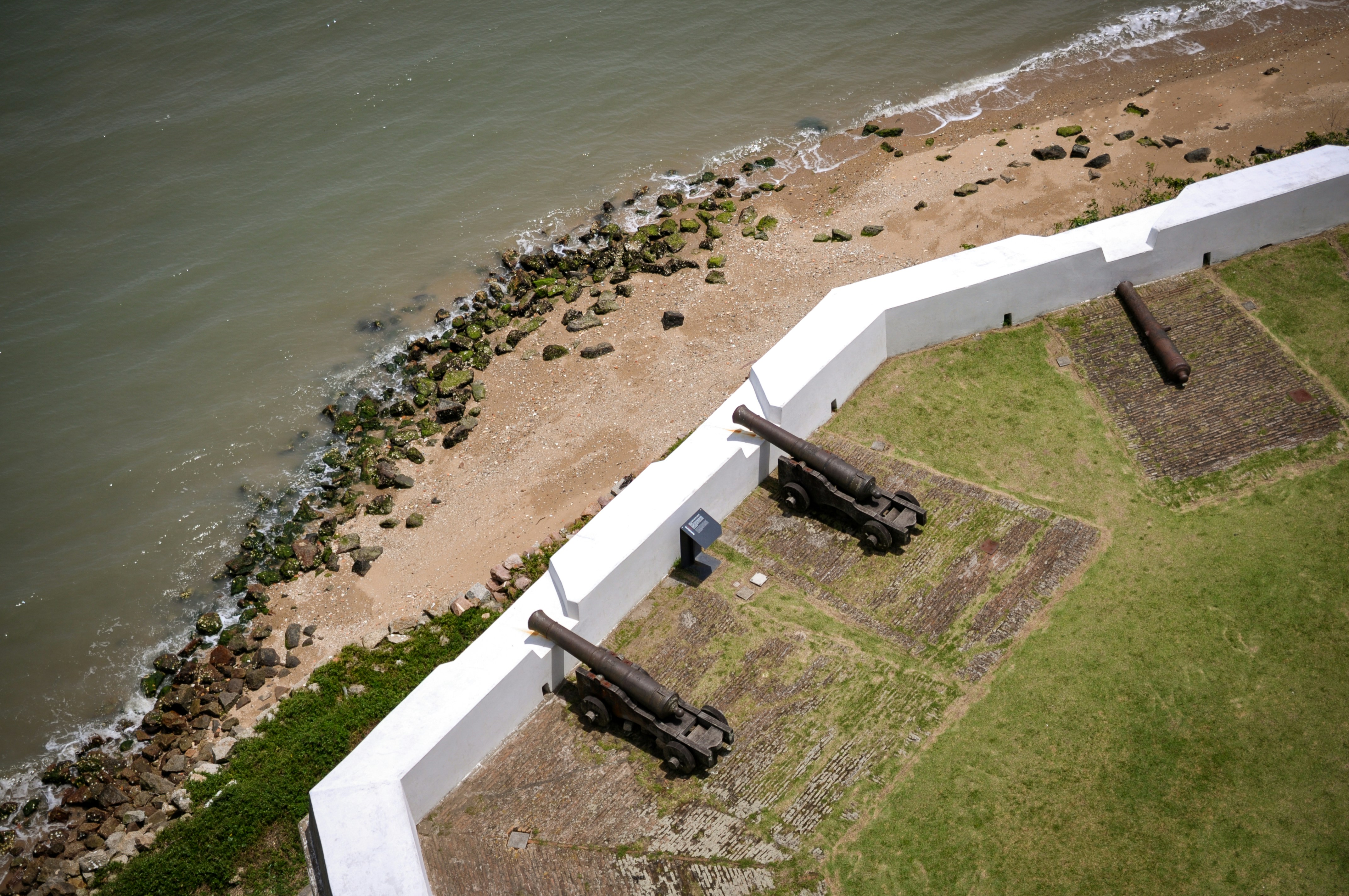 Diagonal Sentinel: Aerial View of Coastal Fort Cannons Along a White Seawall