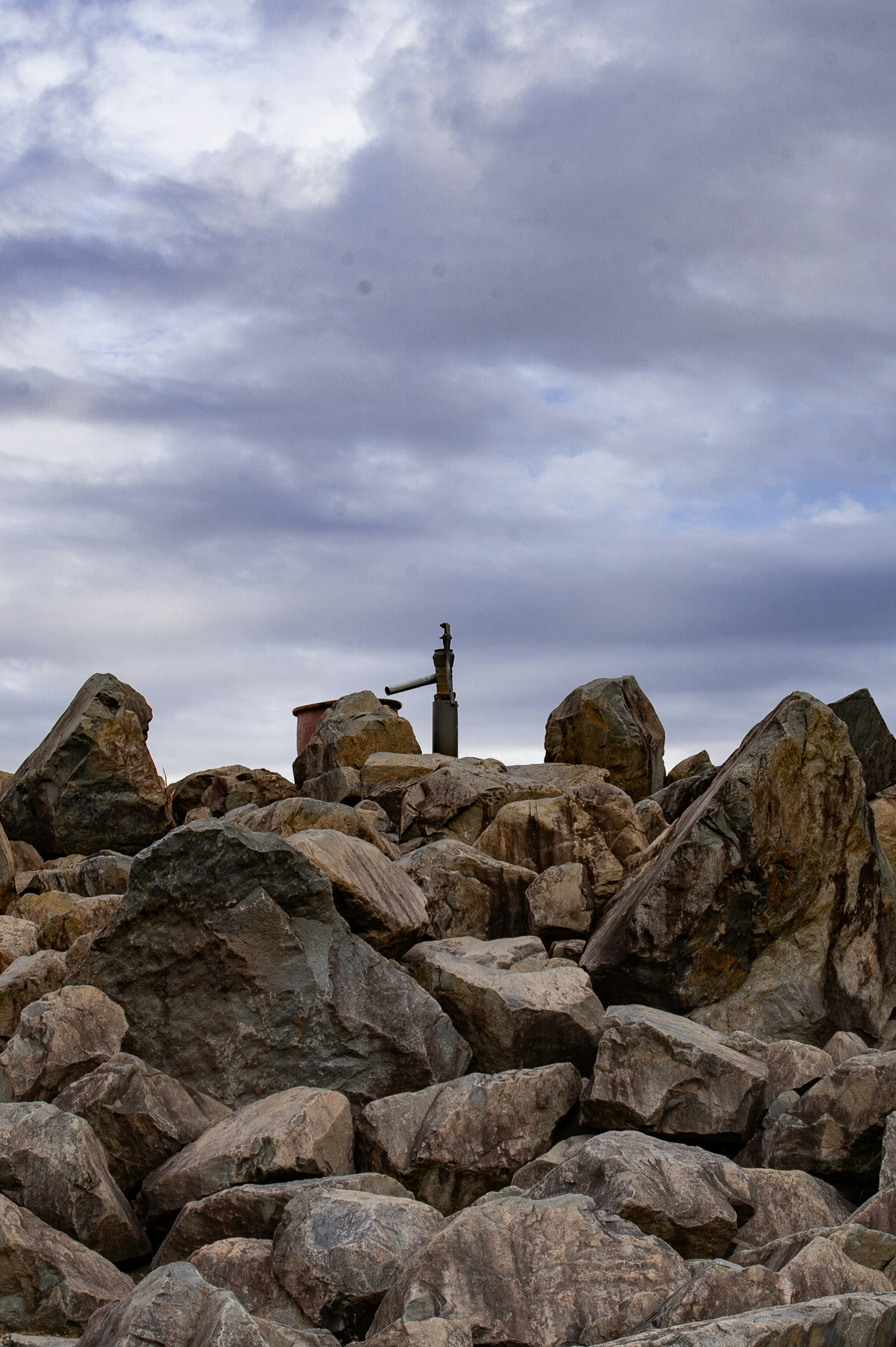 Sentinel on the Breakwater: A lone statue atop jagged rocks under a moody sky