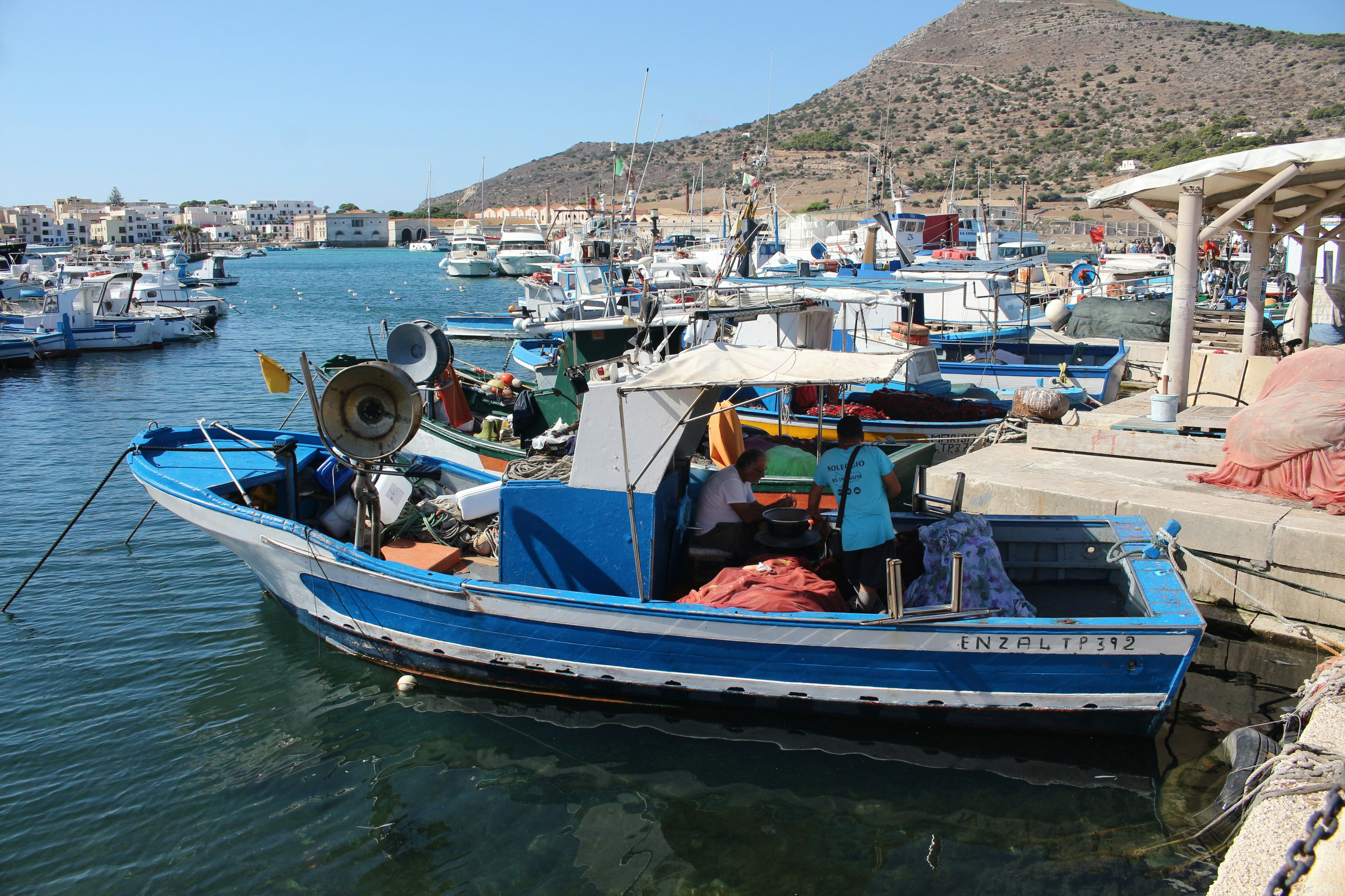 Azure-Hulled Workboat Moored at a Sunlit Marina with Hillside Town Backdrop