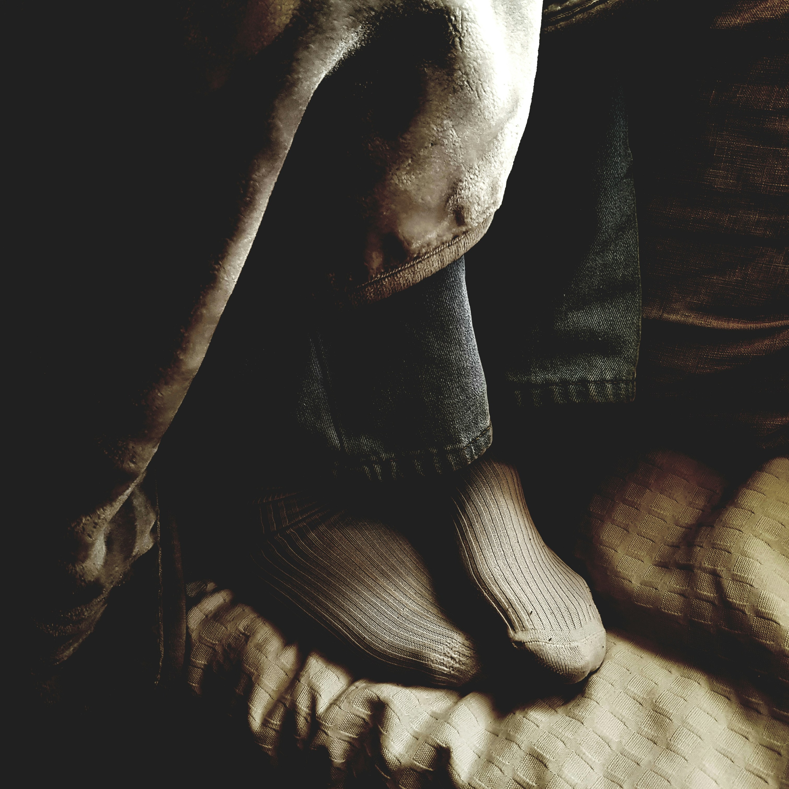 A low-key photograph of legs and warm socks resting on a dimly lit couch.