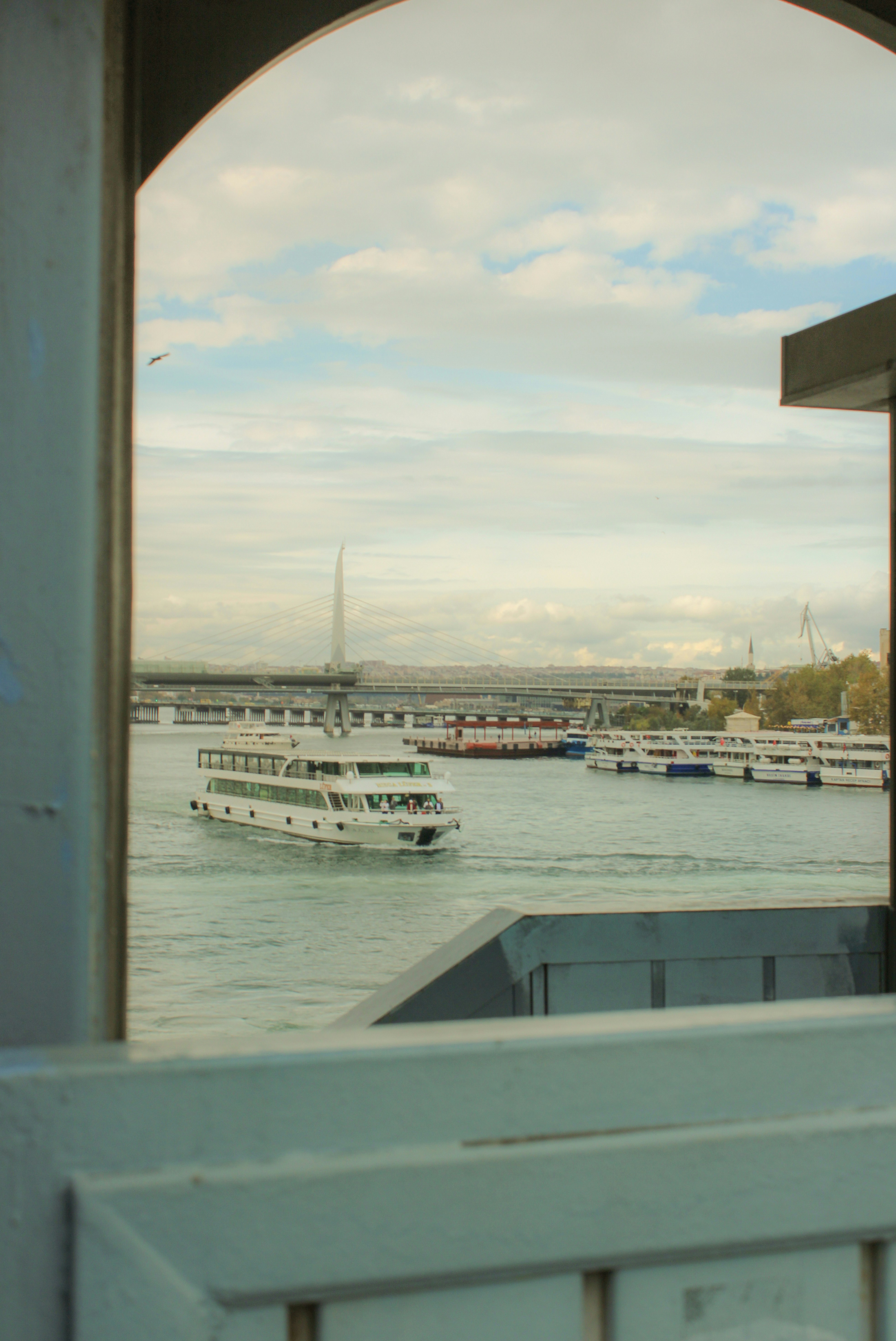 Framed River Life: Boats, Arch, and a Distant Cable-Stayed Bridge