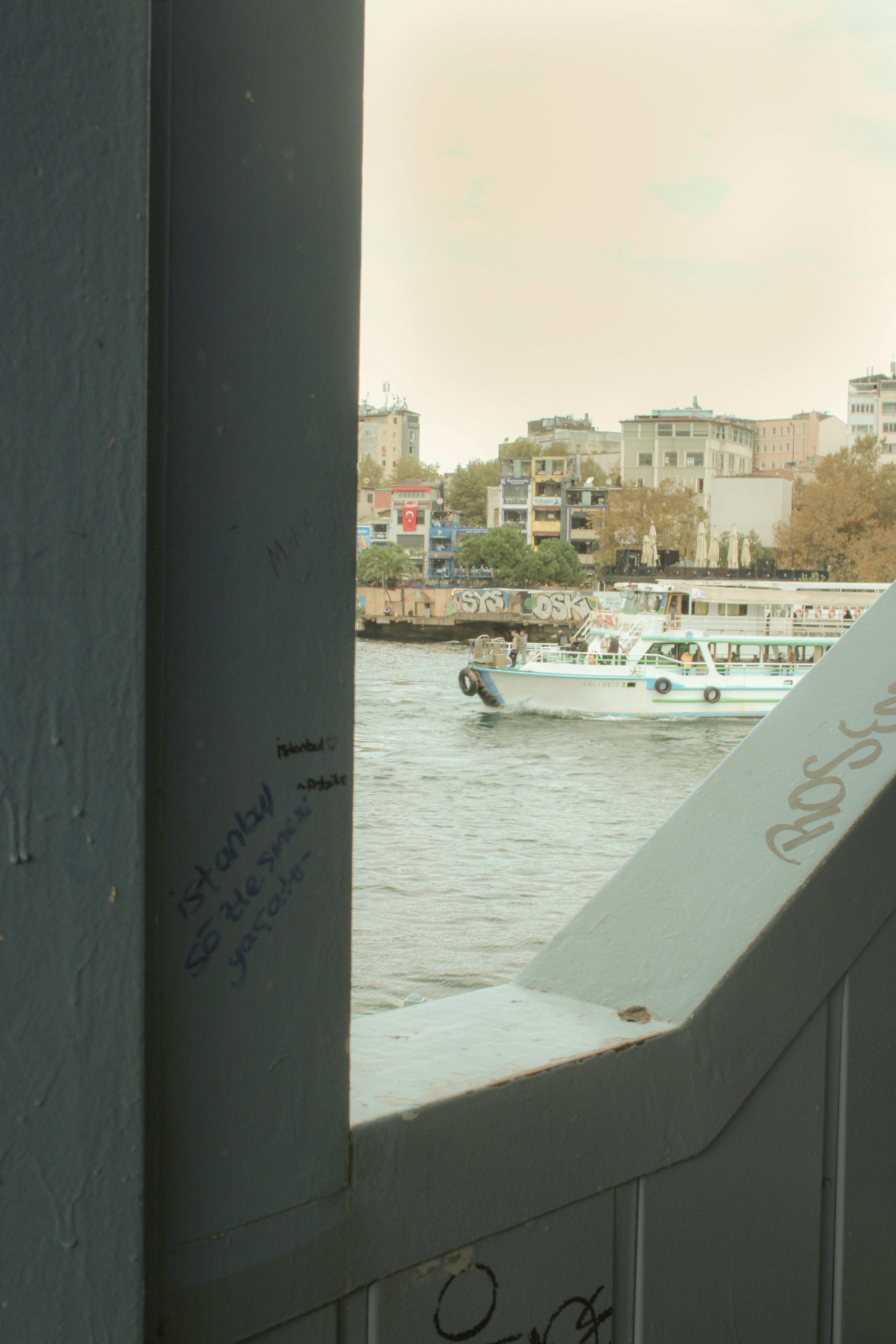 Mid-river commuter boat framed by graffiti and steel at a quiet city waterfront