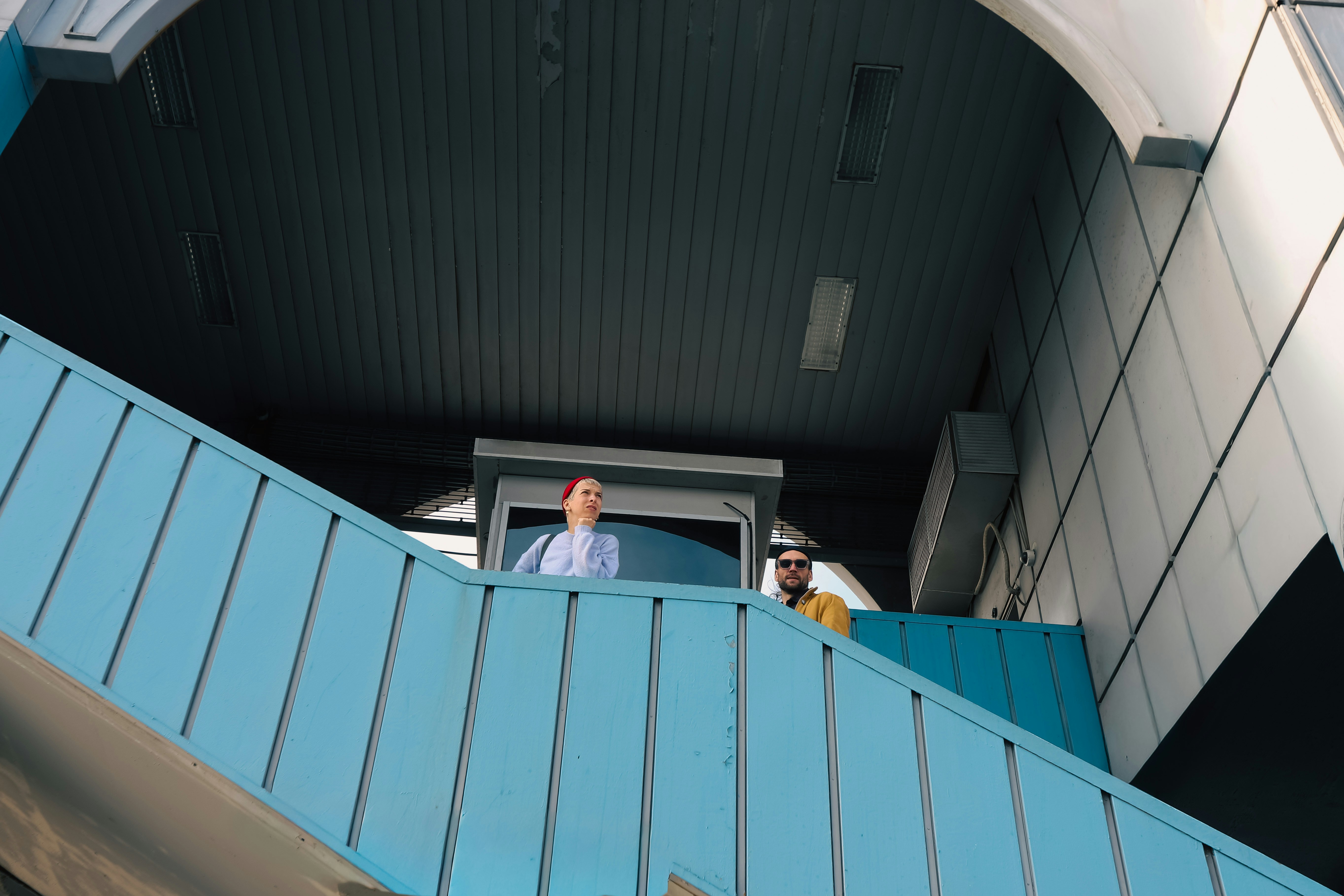 Between Blue Rails and Concrete Angles: Two Watch from the Balcony
