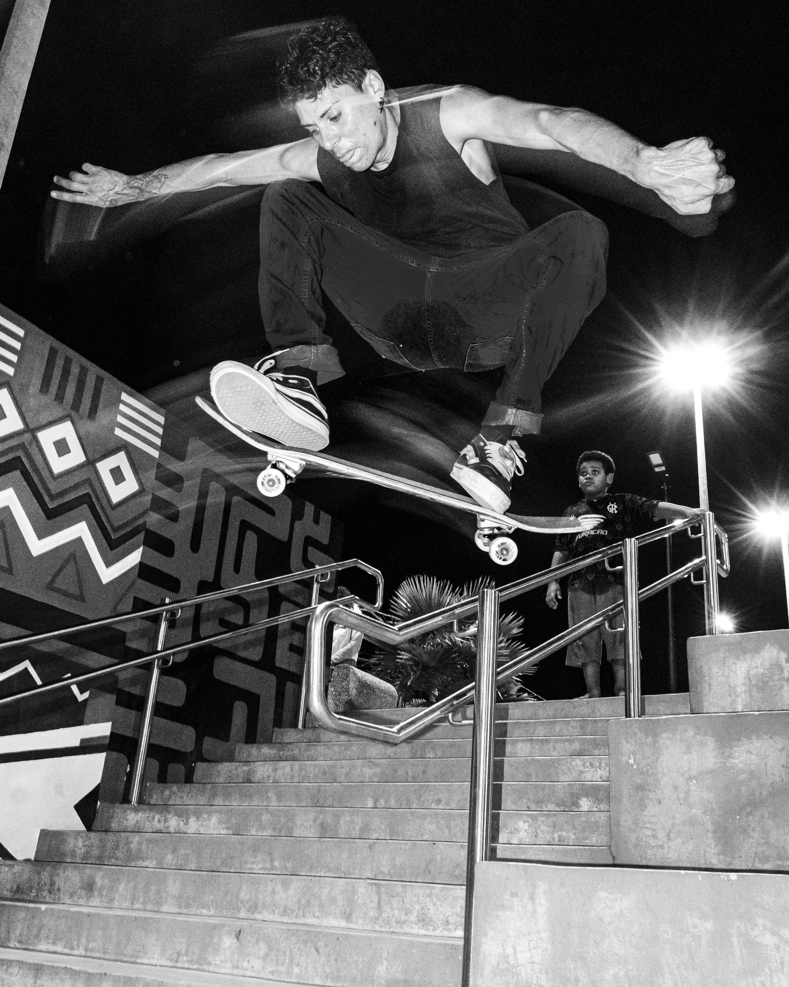 Night urban flight: skateboarder soars, observed by a mesmerized child.