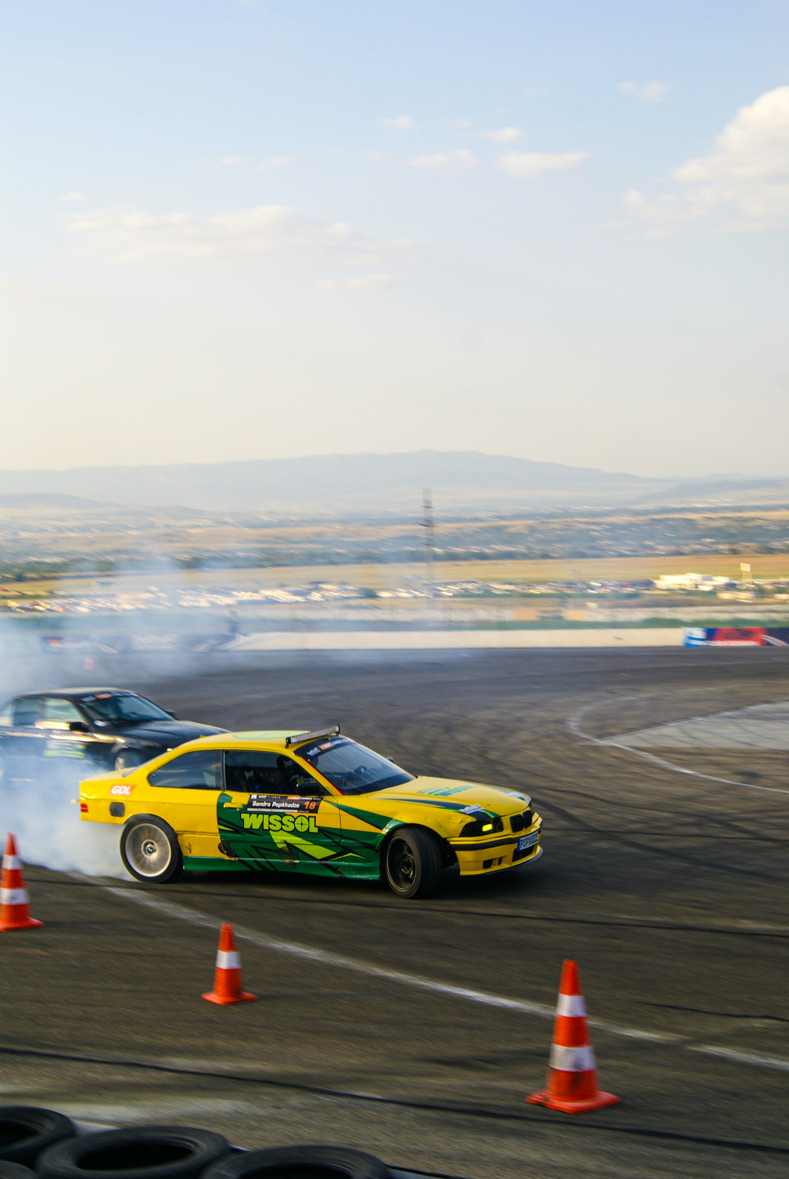 Sunlit Drift: Yellow Car Slices Through Cones with Tire Smoke