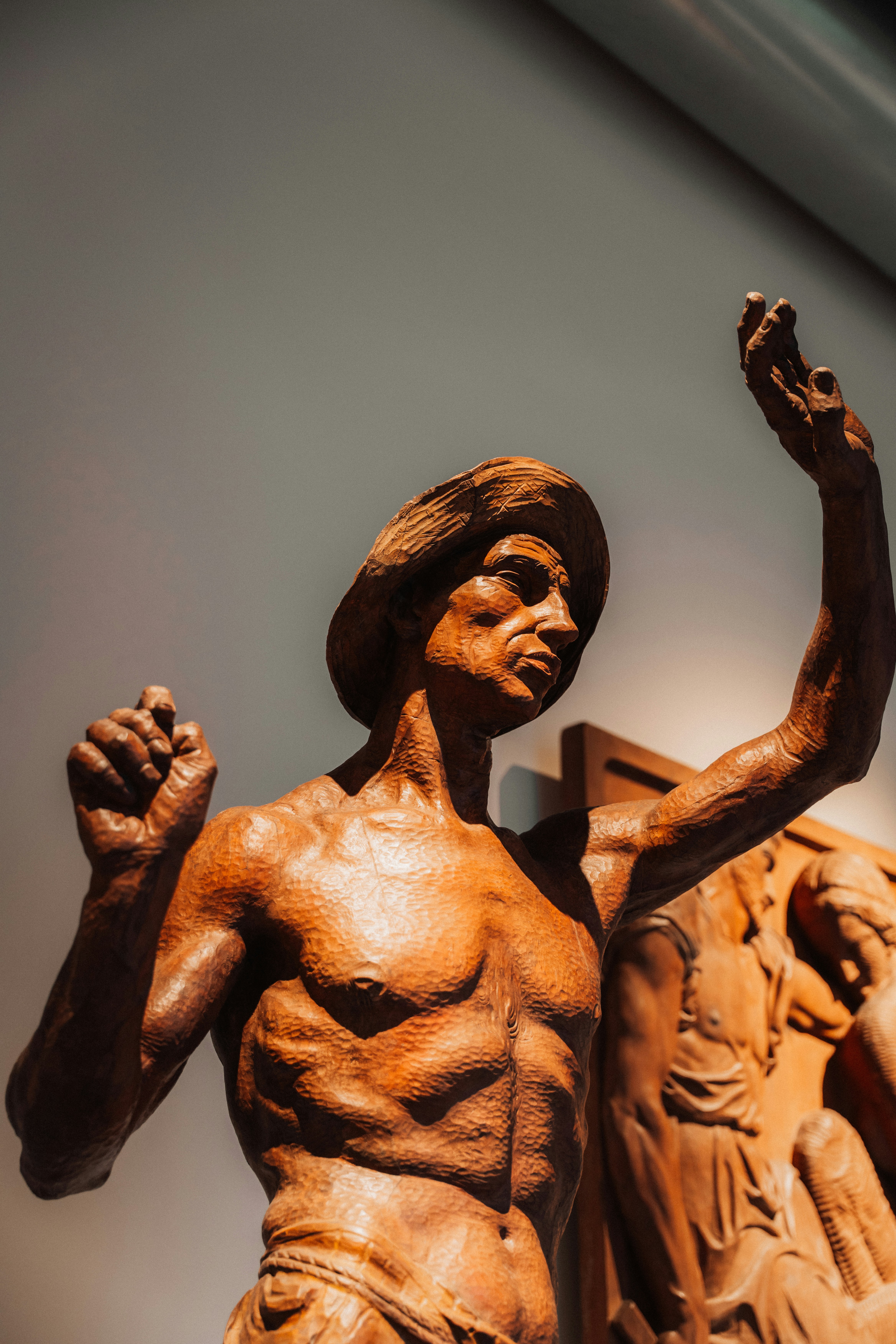Amber-Toned Carved Figure with Raised Arms Under Gallery Light