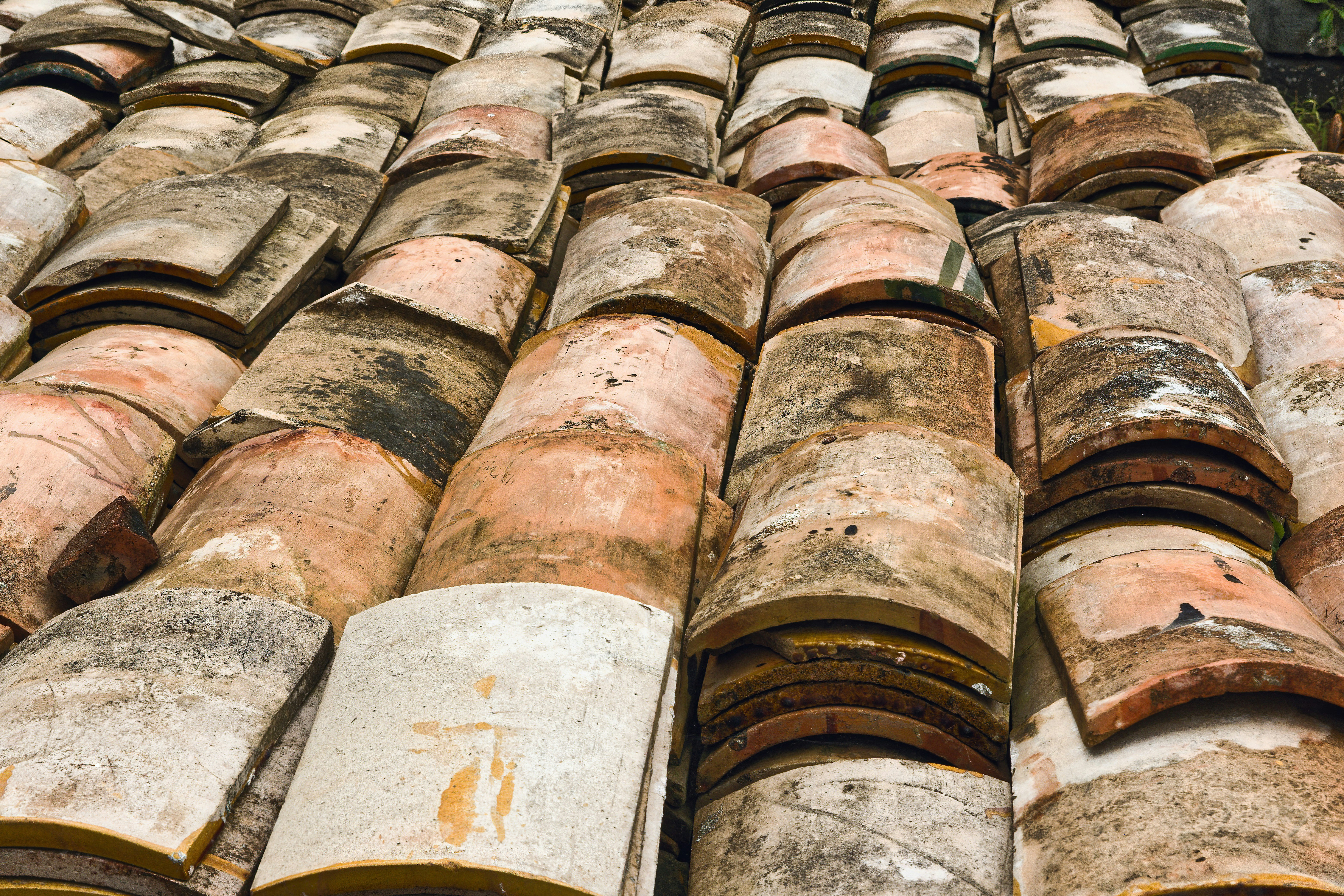 Textured clay roof tiles in various shades highlighting wear and age on a rooftop - Close-up view of clay roof tiles displaying different colors and textures, showcasing their weathered condition and intricate arrangement under natural light.