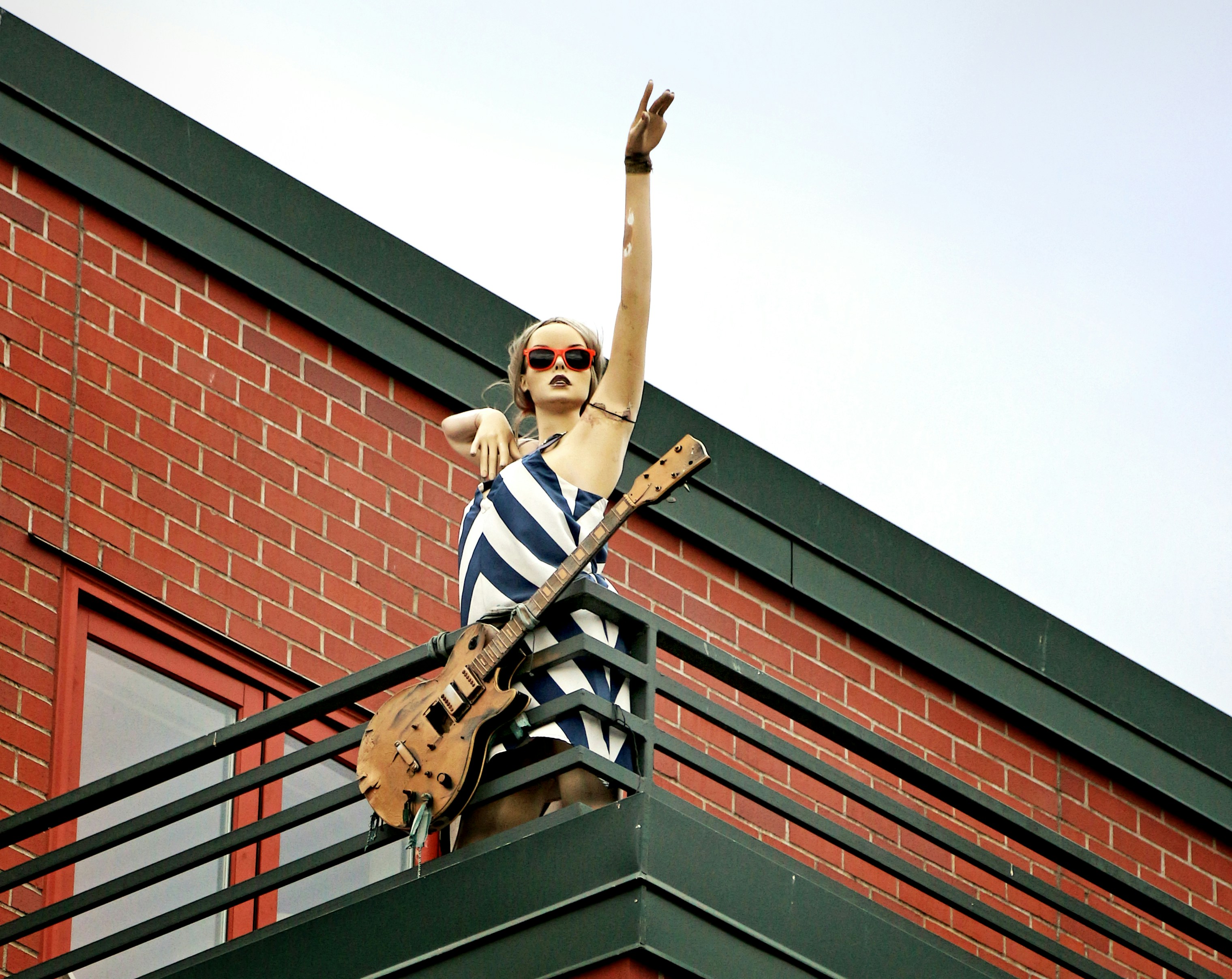 Balcony Anthem: The Striped Guitarist Reaches Up on Red Brick