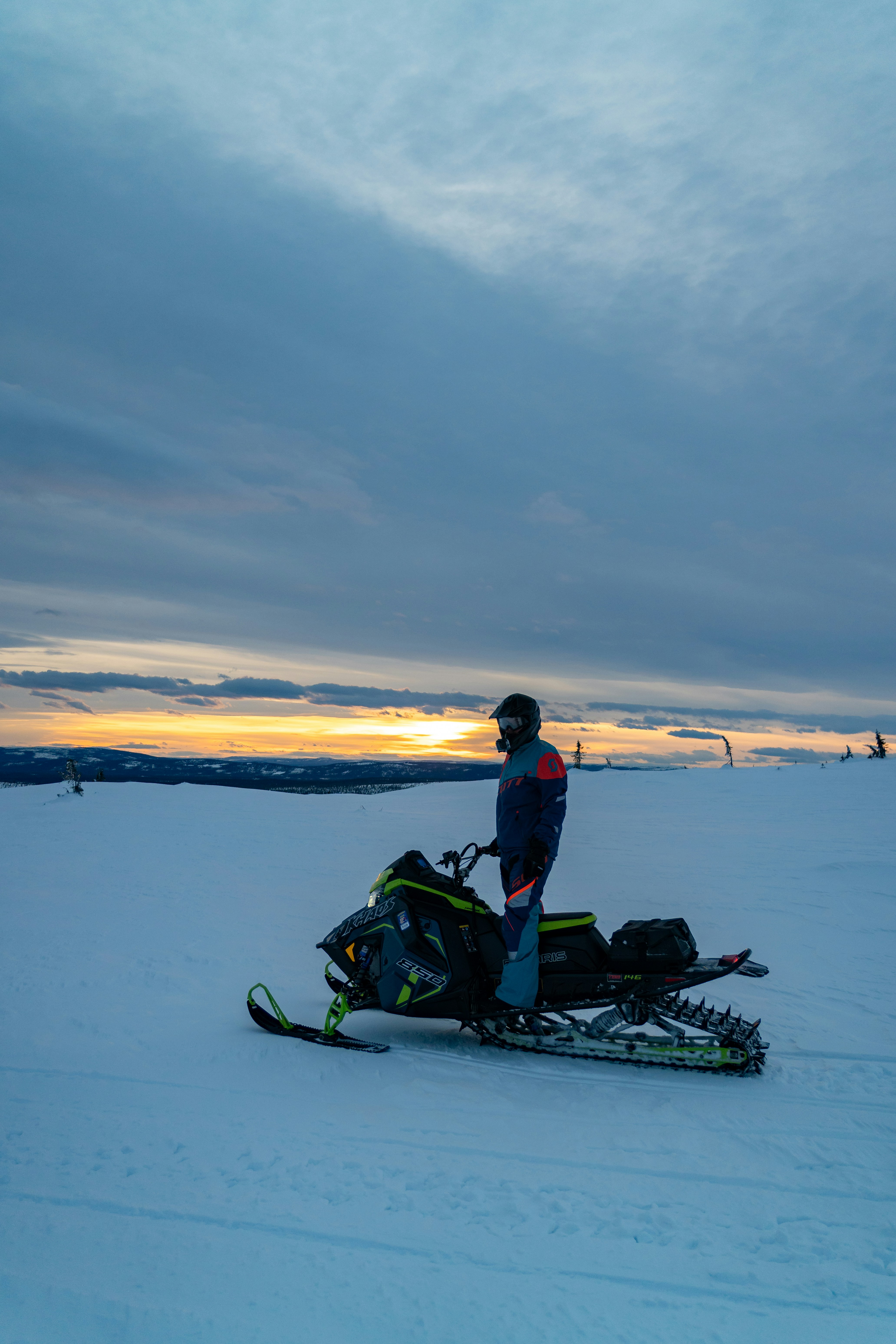 Twilight on the Tundra: Snowmobiler Pauses as Sunset Bleeds Across Snow