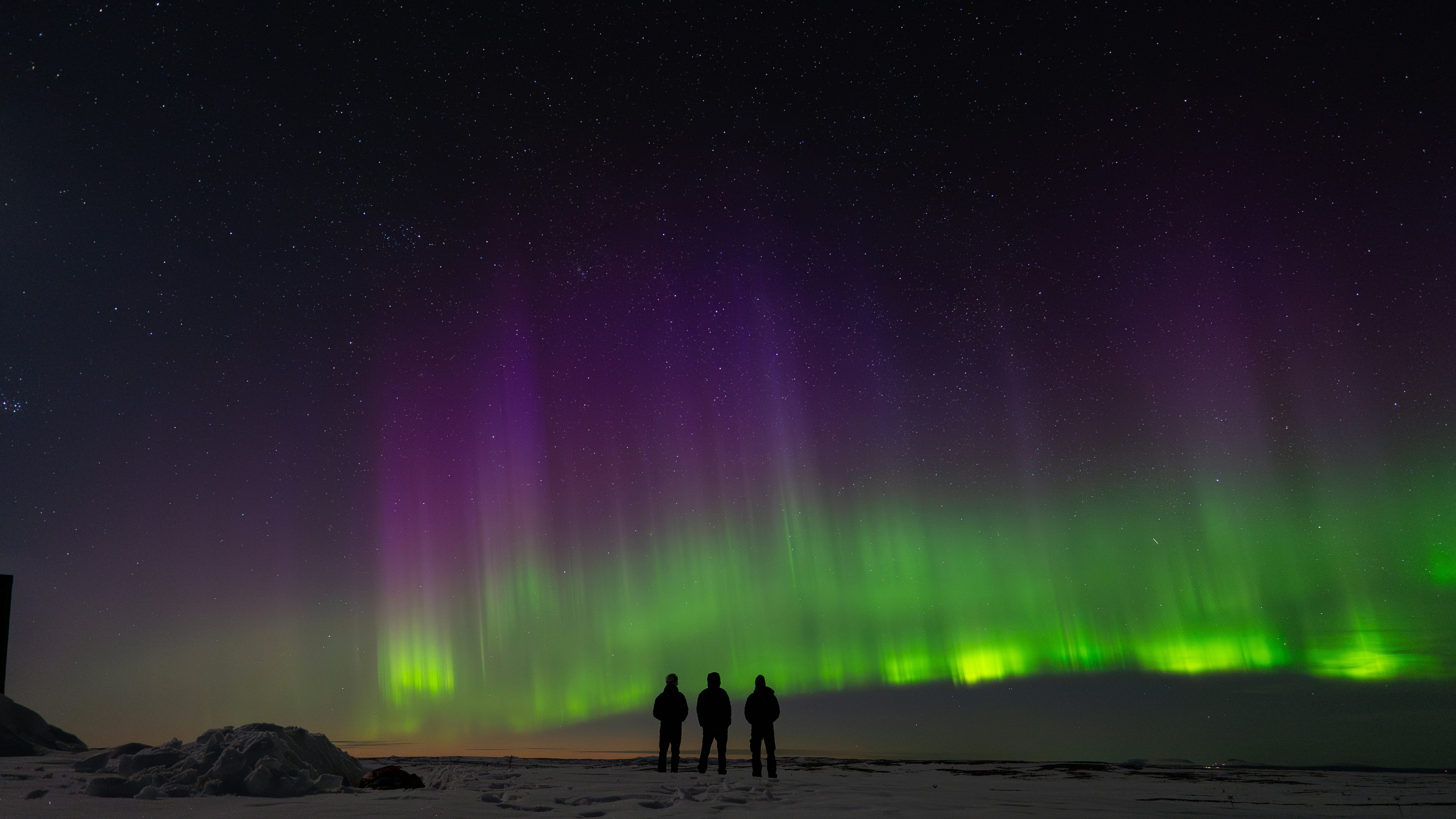 Aurora Curtain Over Snow: Three Silhouettes Beneath a Neon Arctic Sky