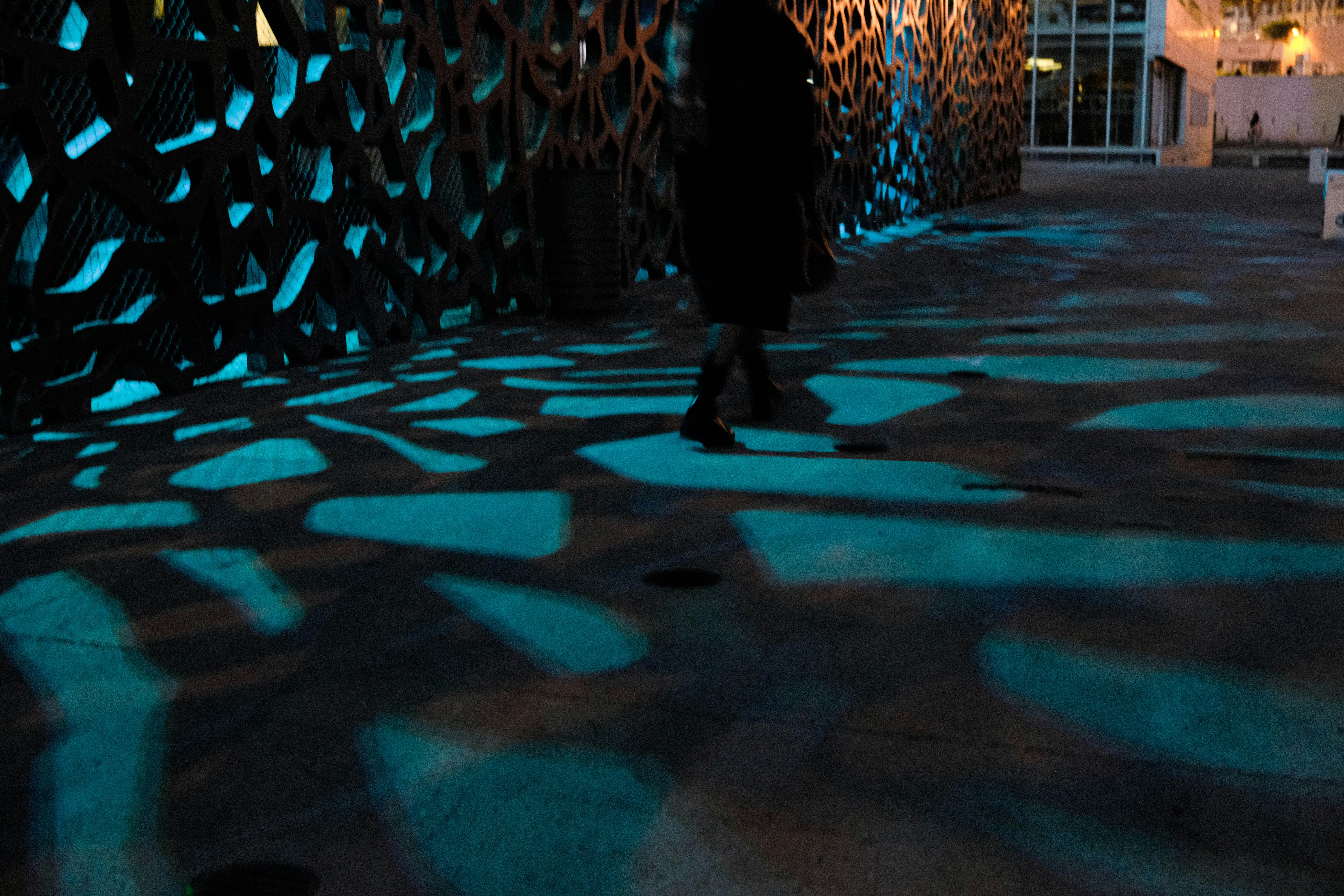 Blue Lace Corridor: A Lone Figure Wanders Through Neon-Patterned Light