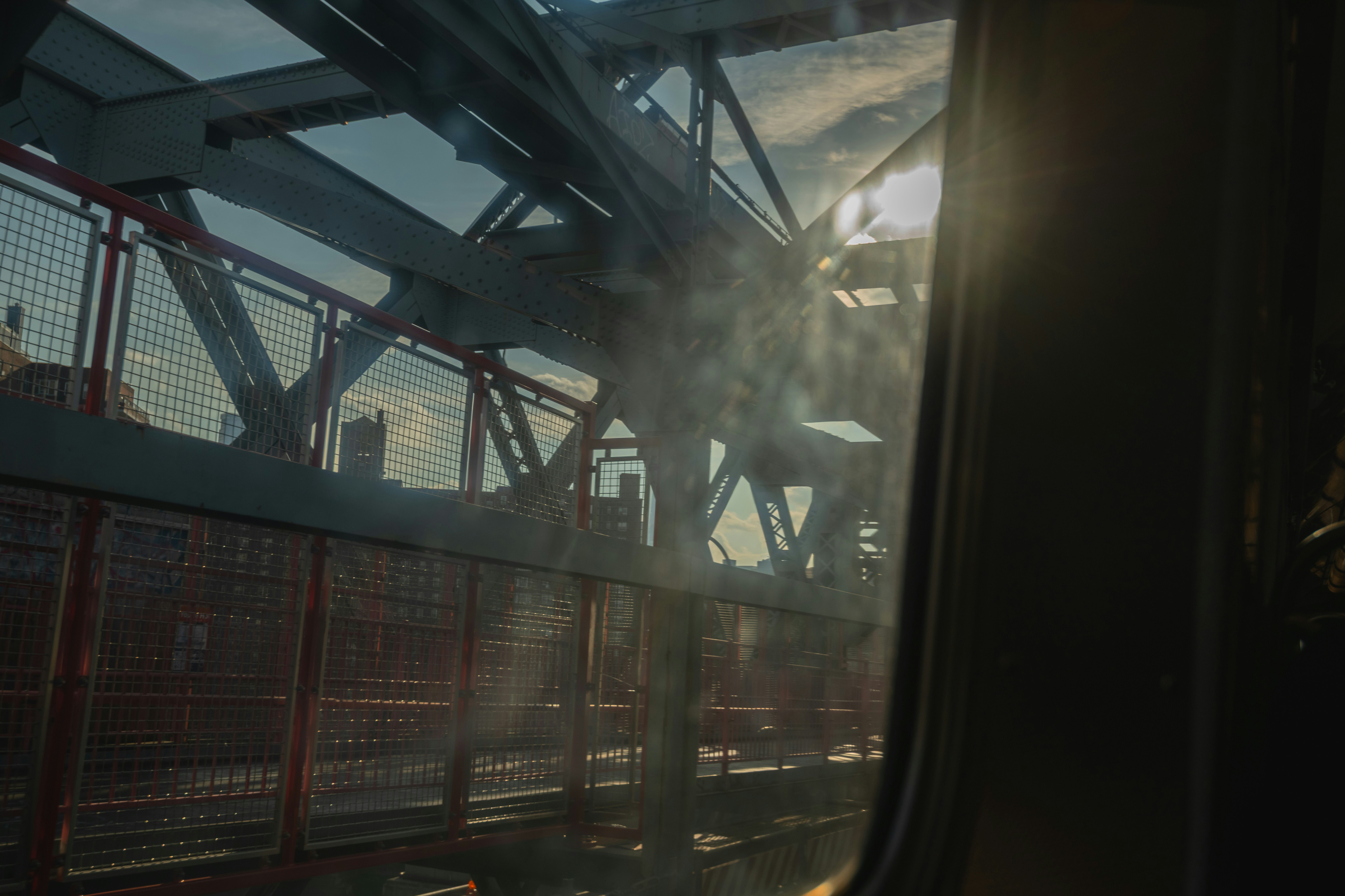 Sunburst Through Steel: A Train Window Framed by Red Fencing and Industrial Geometry
