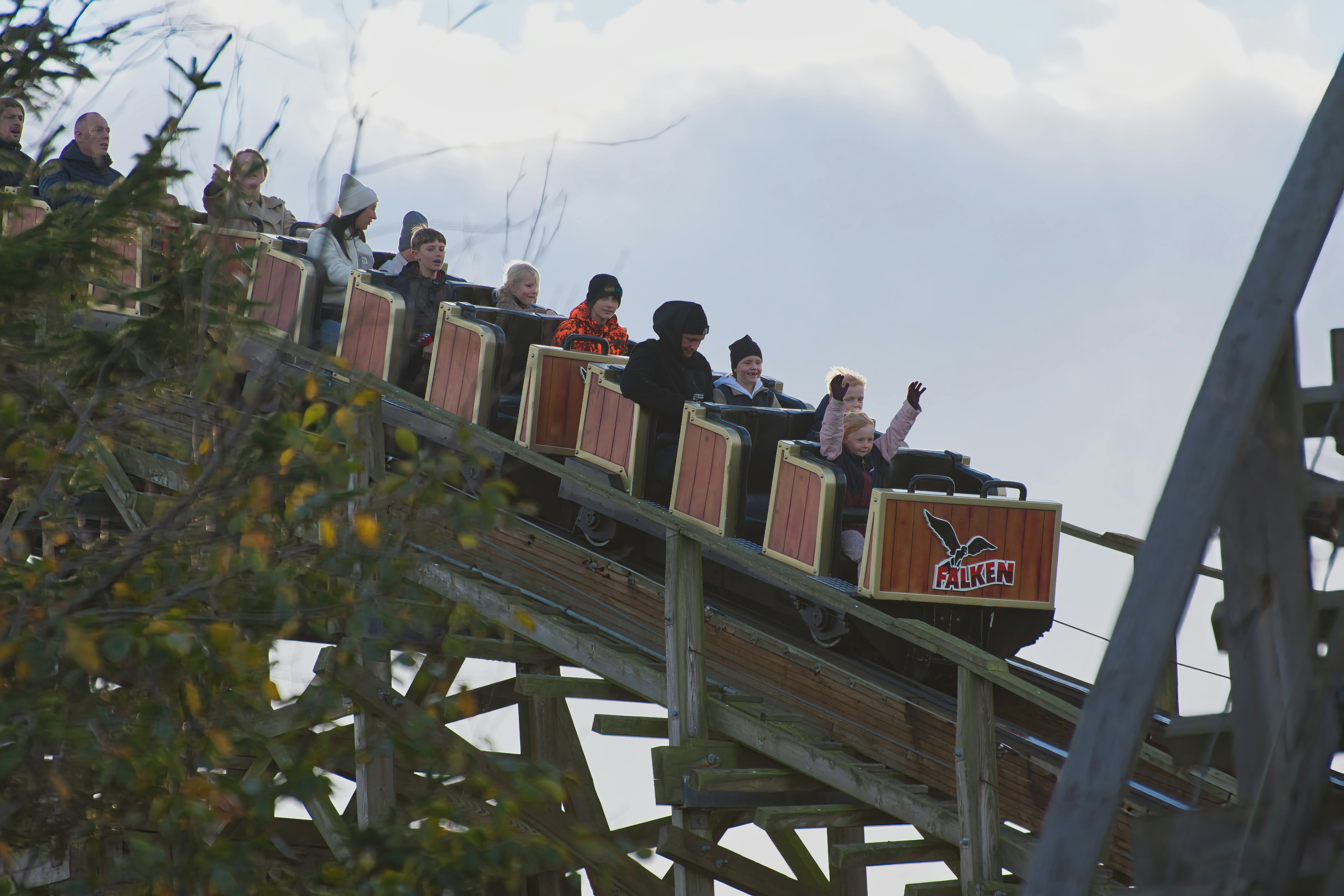 Across the Wooden Crest: Passengers Ride a Vintage Coaster Beneath a Cloudy Sky