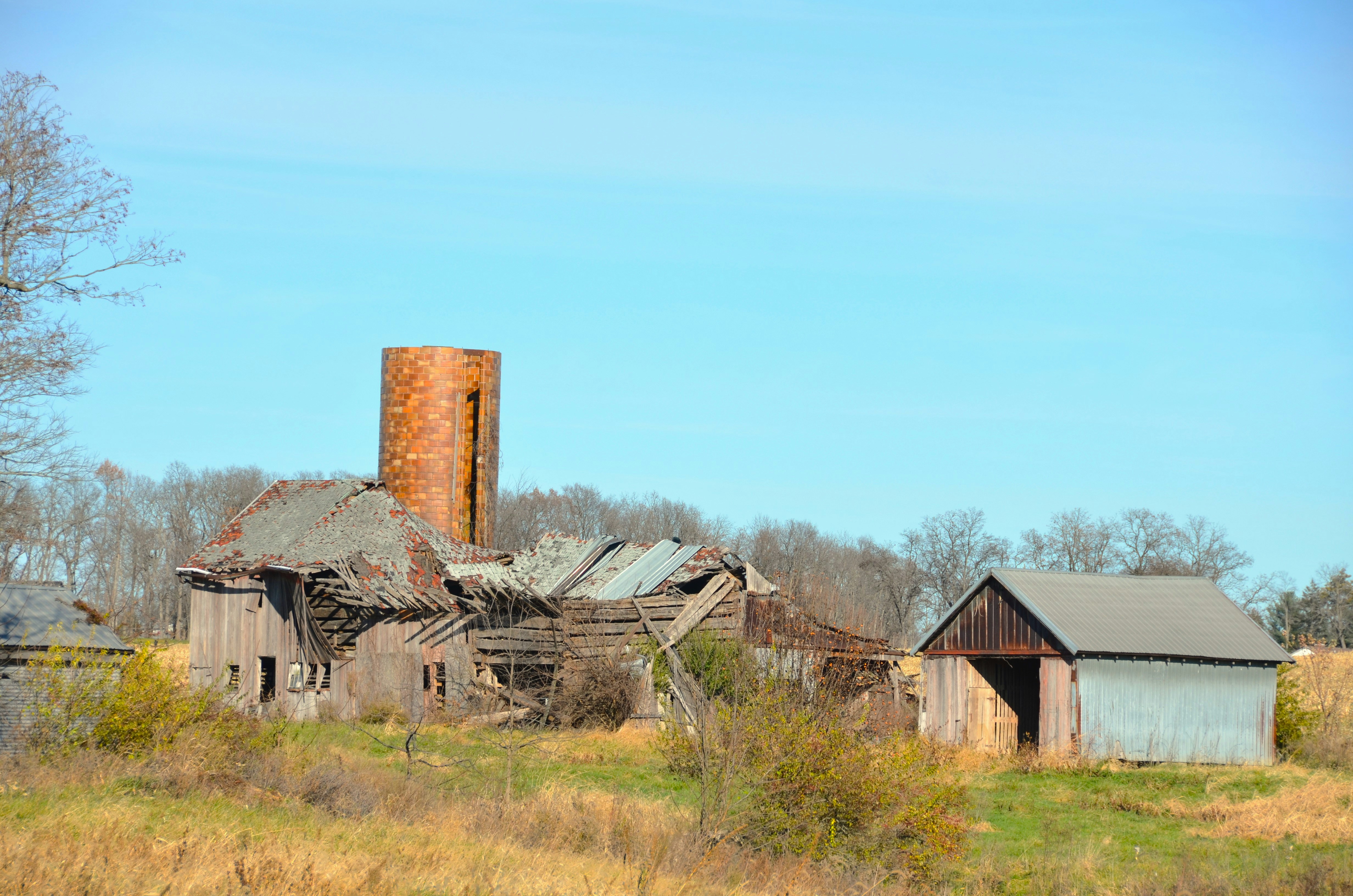 Rust-Red Silo Guards a Crumbling Farmstead Under a Bright Sky