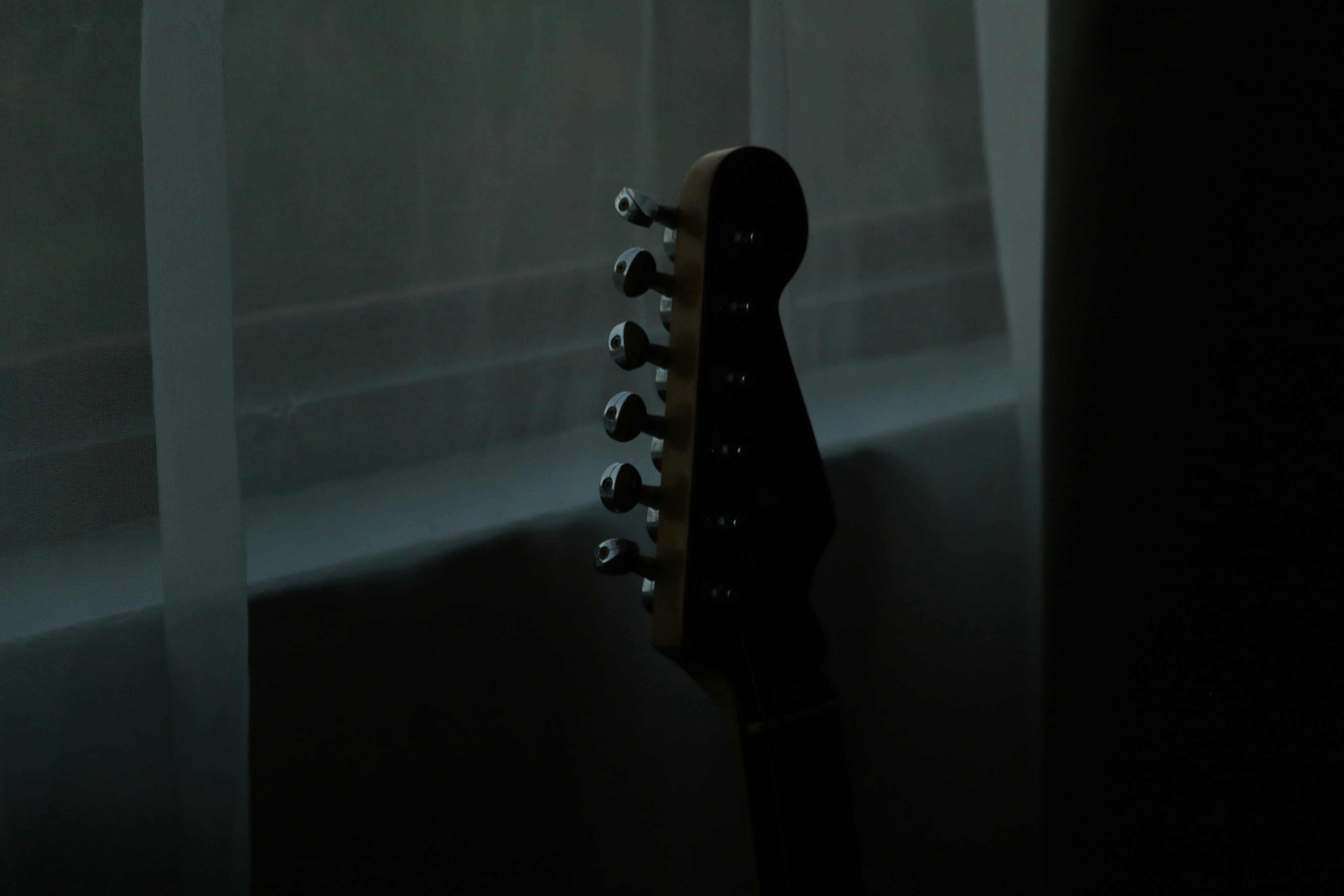 Nocturnal Headstock: A Guitar Emerges from Window Light