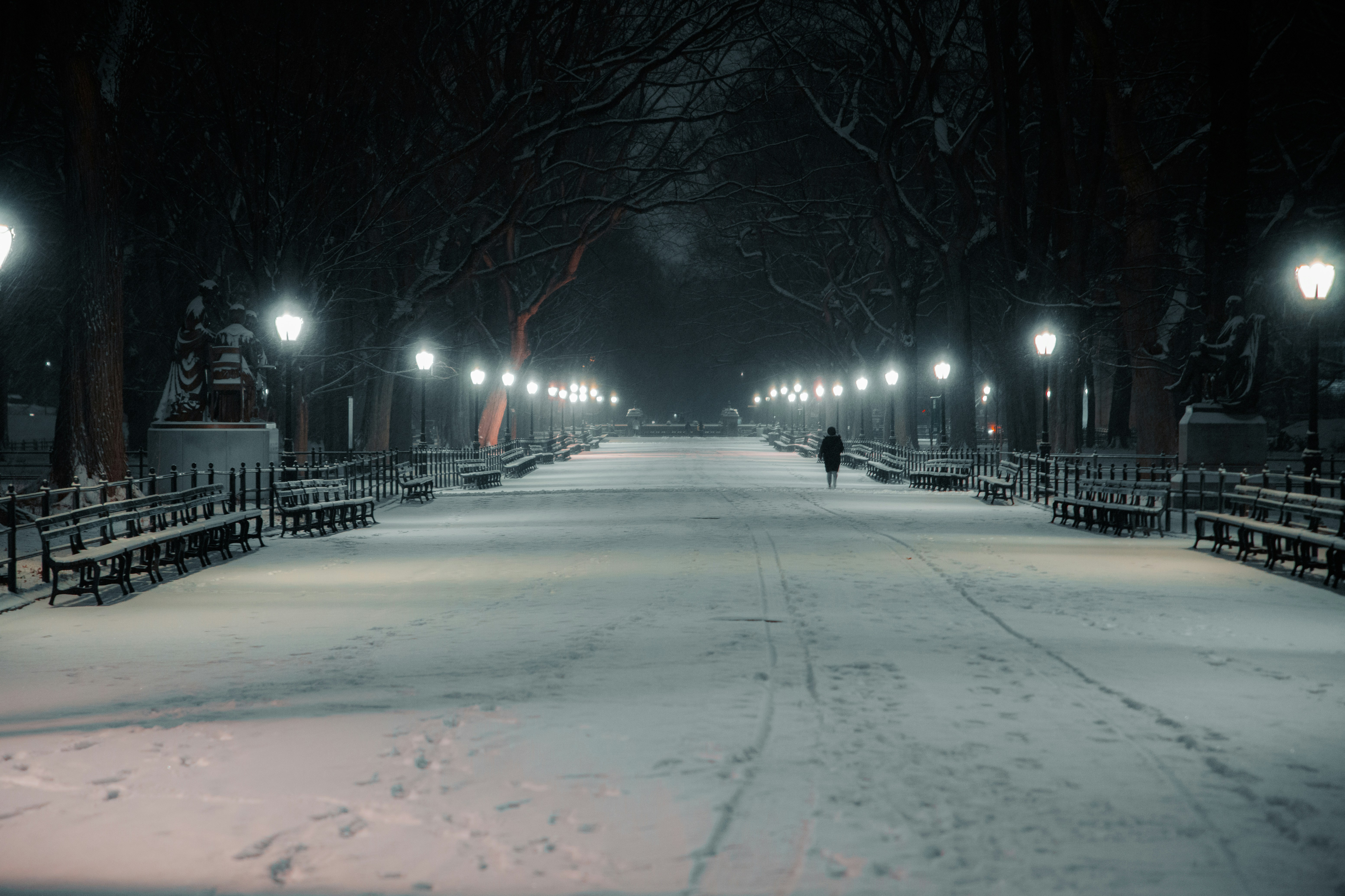 A lone figure walks down a snow-covered path at night.