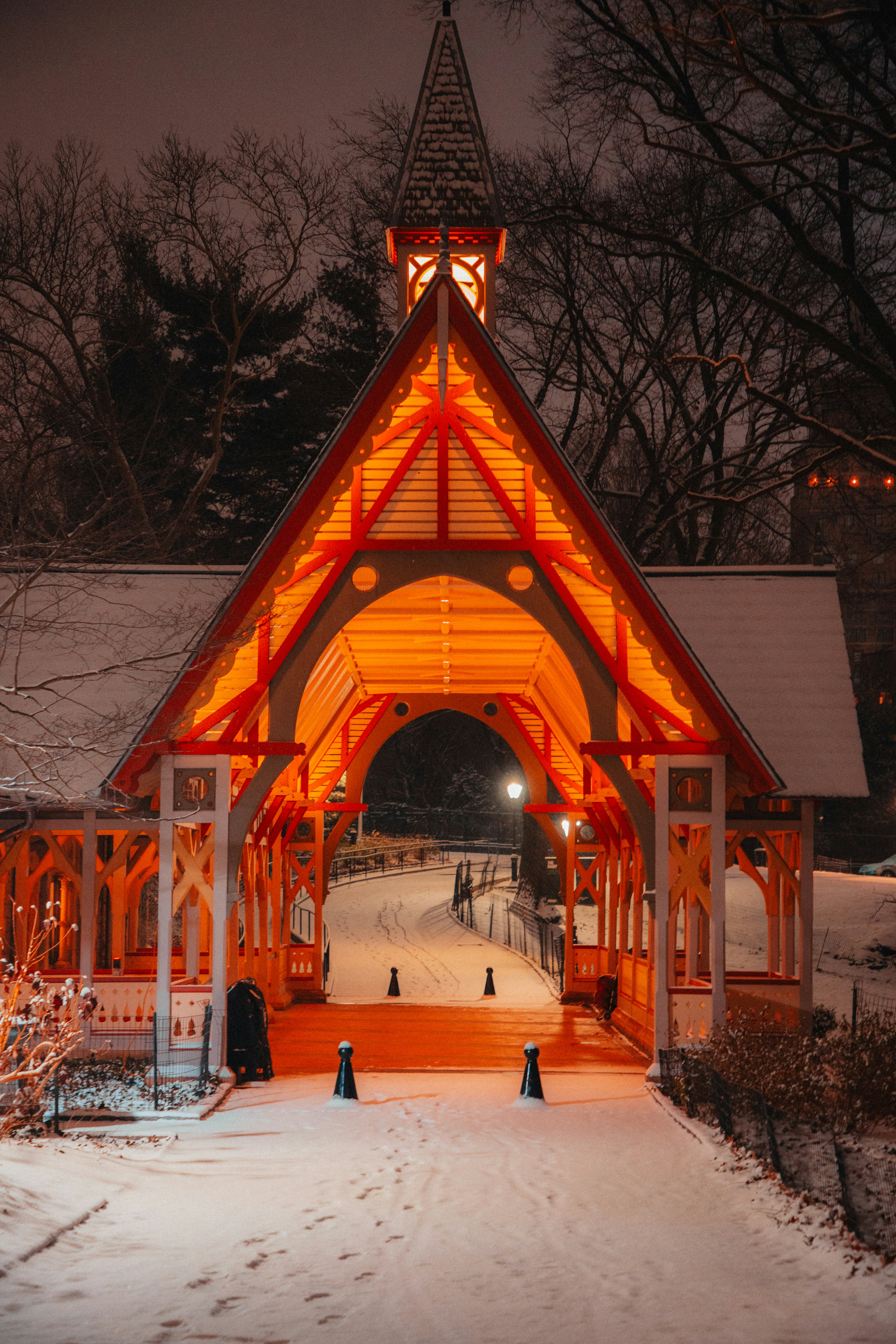 A brightly lit wooden bridge in the snow at night.