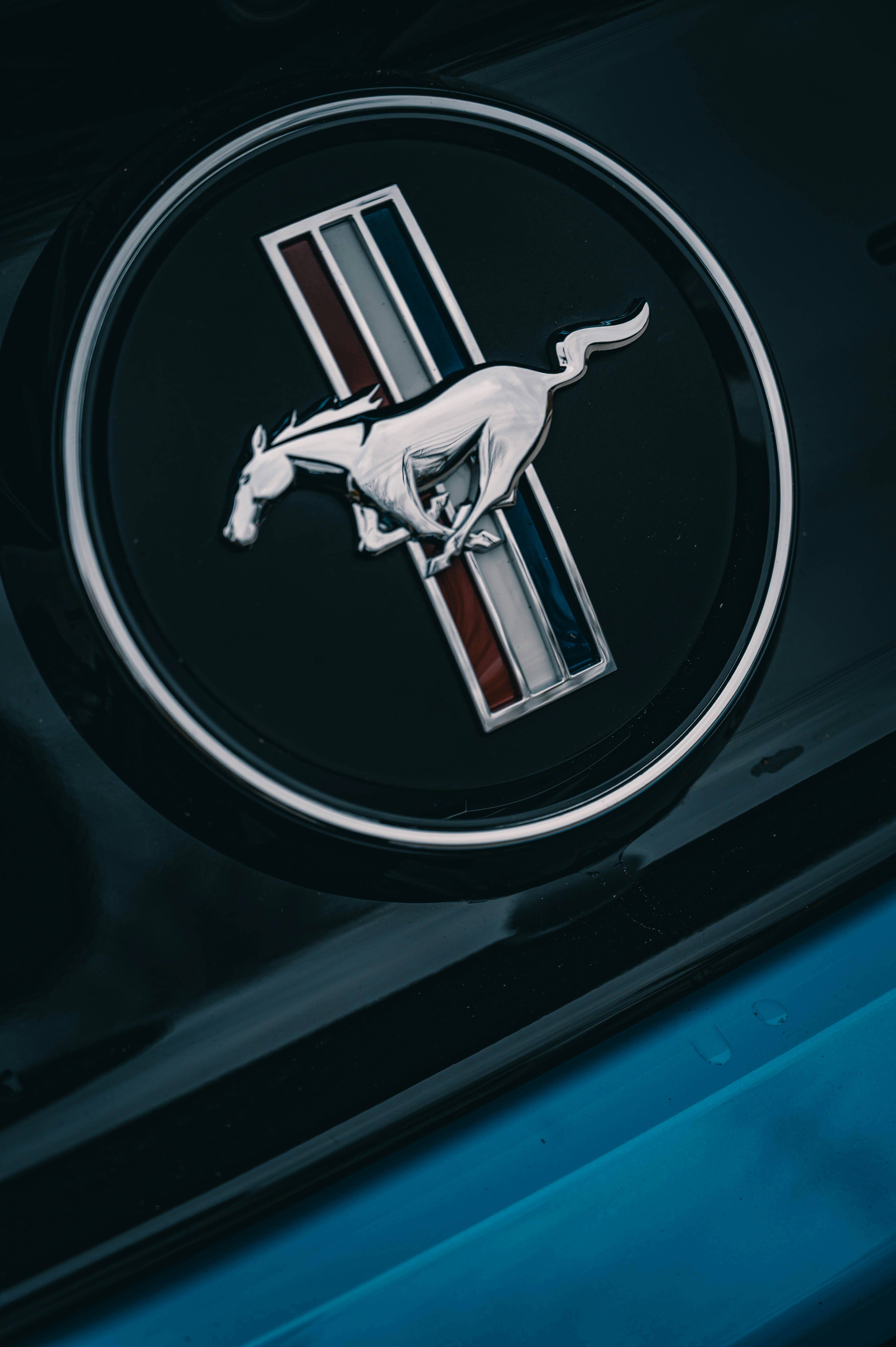 Chrome Mustang Emblem on a Deep-Blue Hood: A Close-Up Portrait of Speed