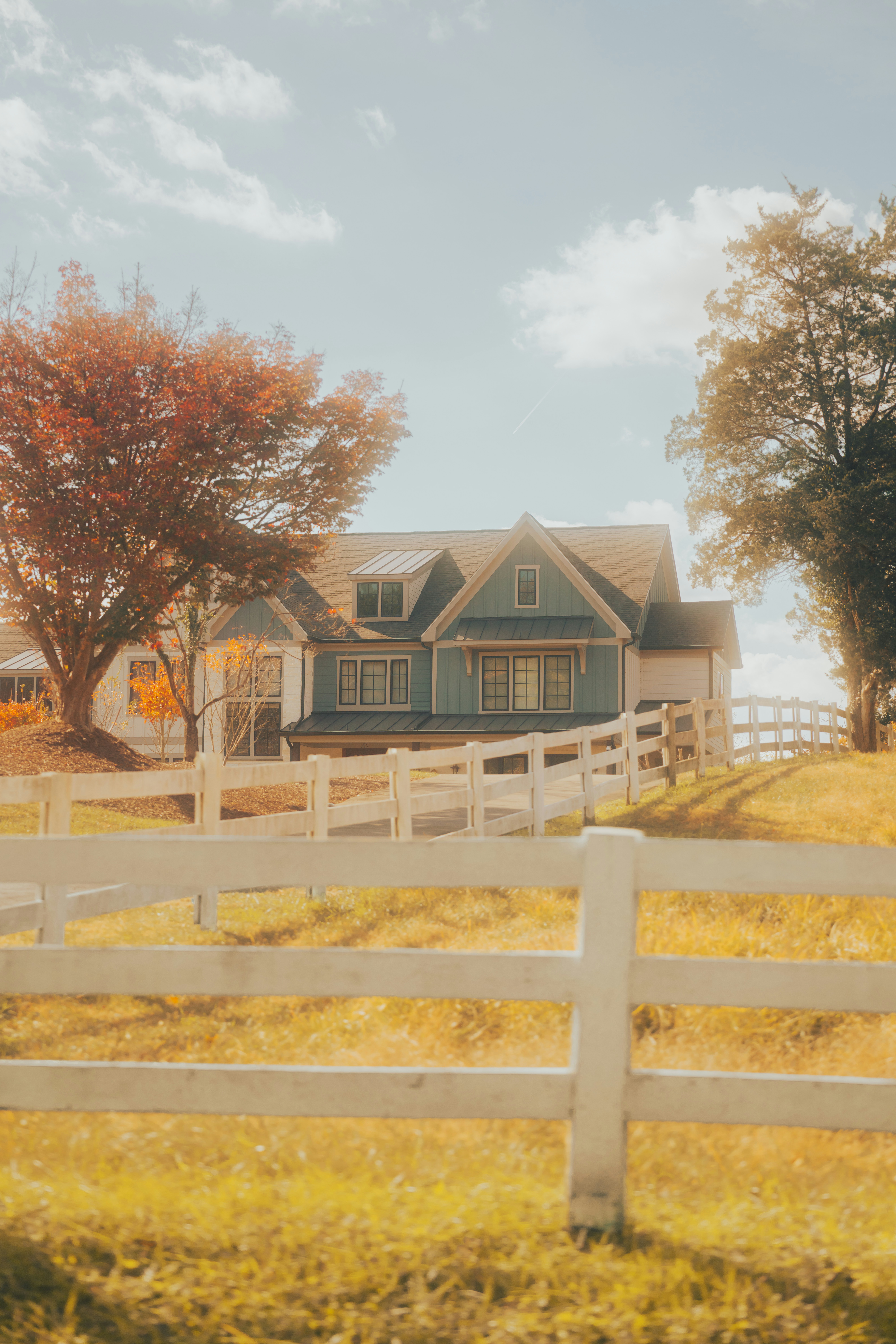 Azure farmhouse on a sunlit hillside, framed by a white fence and amber trees