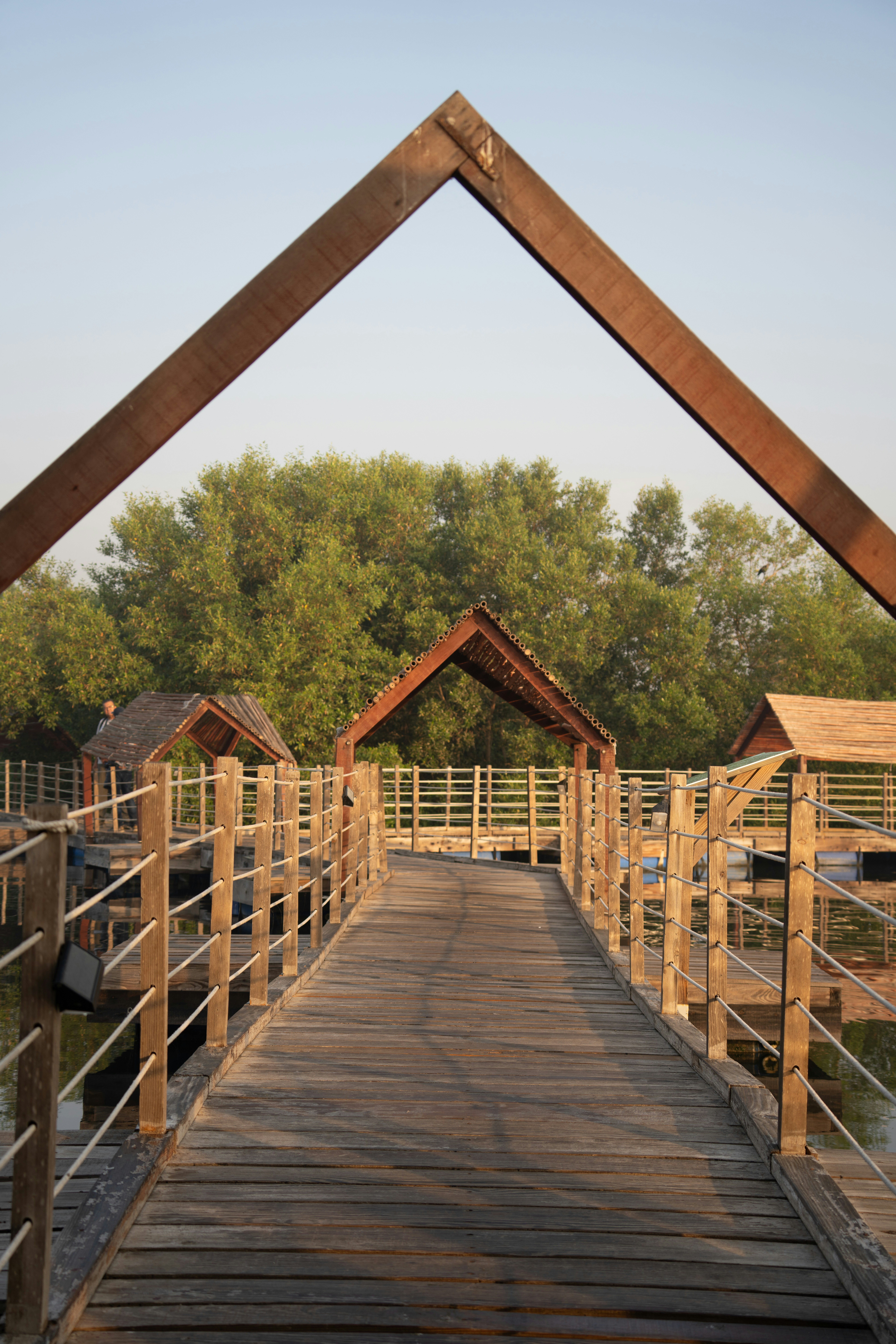 A clean and minimalist frame showing the wooden arches of the mangrove walkway lined up perfectly under a soft morning sky. The simplicity and symmetry make it ideal for modern design, architecture features, and nature storytelling.