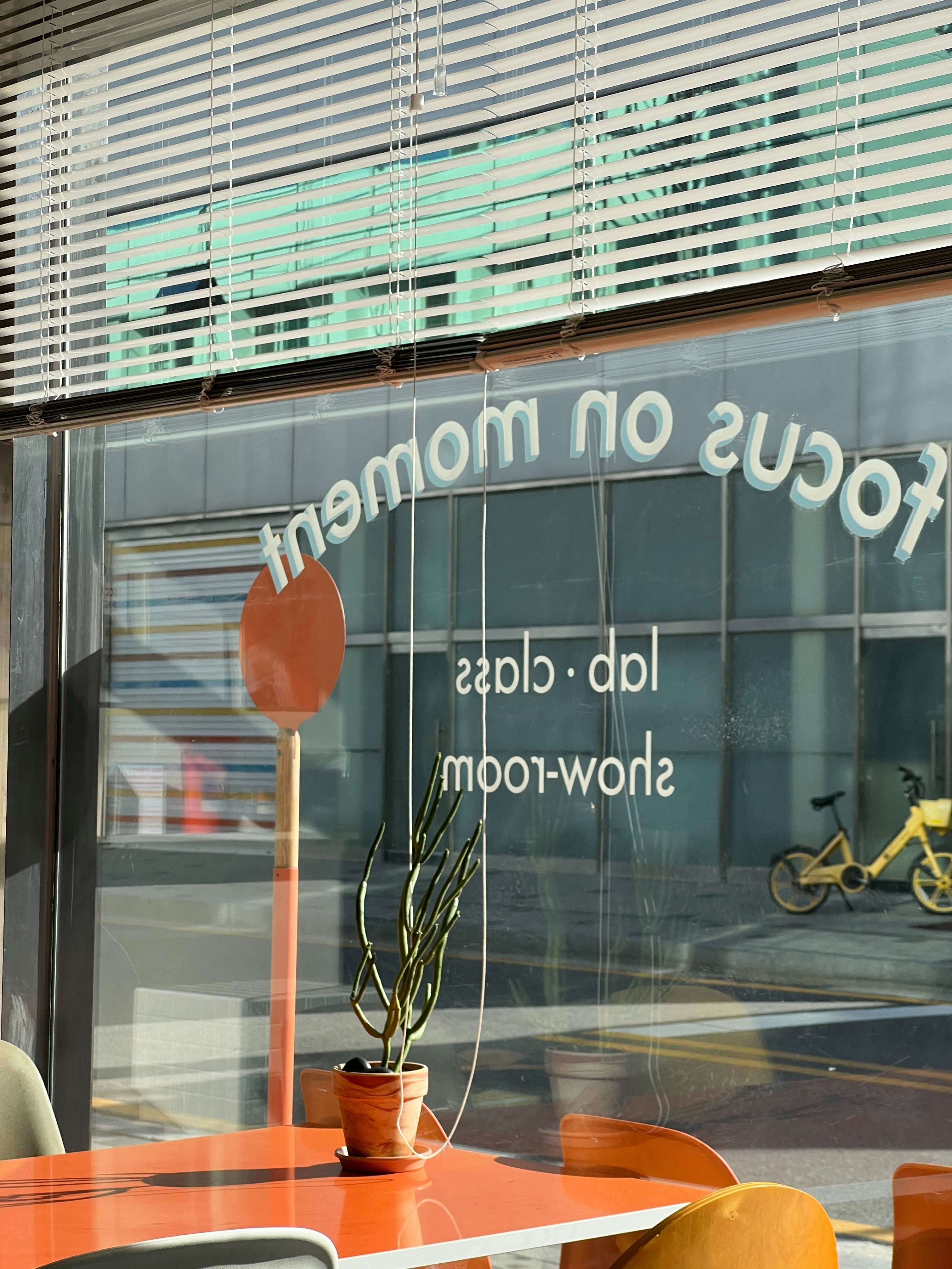 Through Glass and Blinds: An Orange Café Table in a Sunlit Café