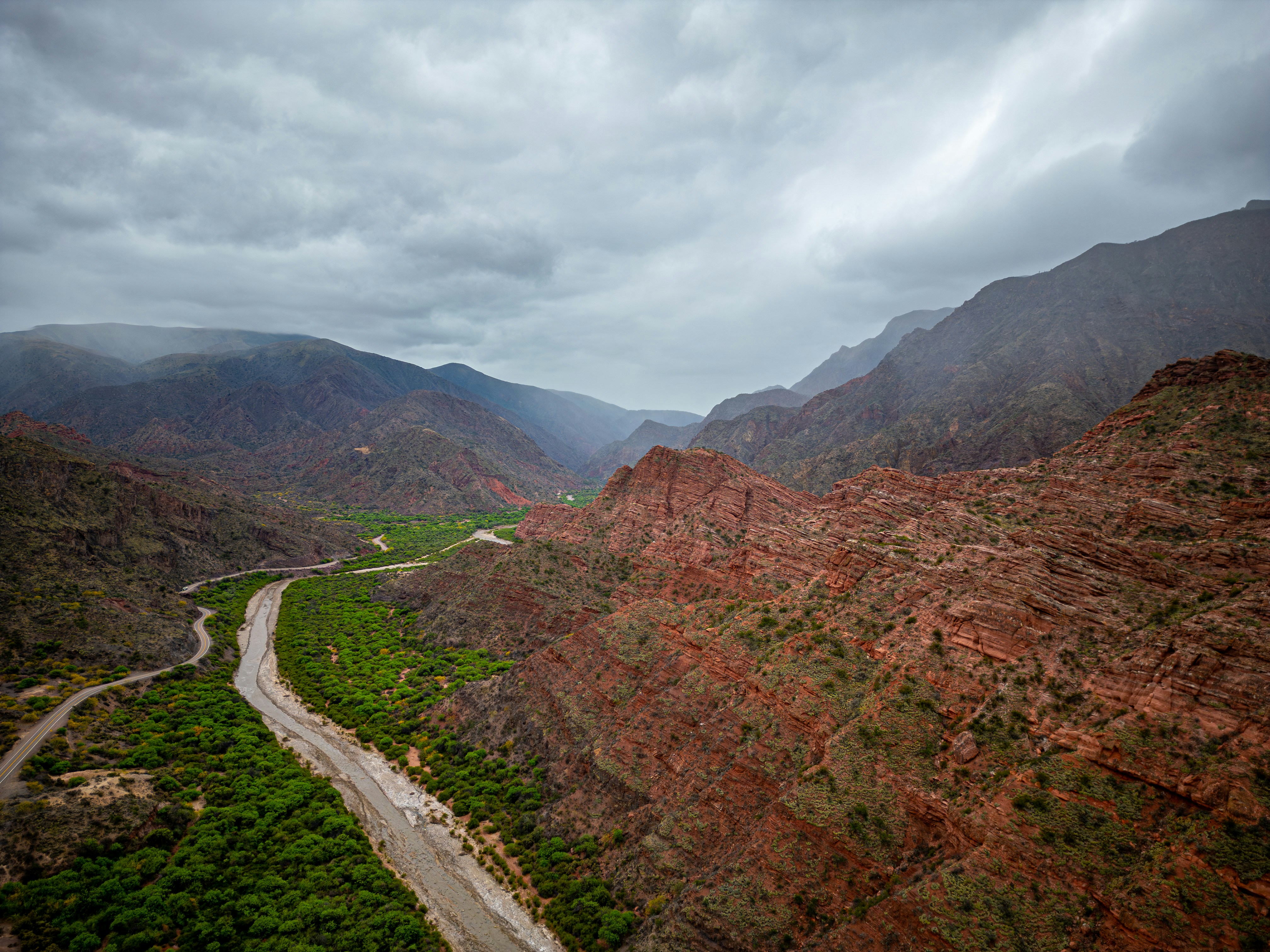 Curved Path Through a Red Canyon: A Green Vein Meets Cloudy Peaks