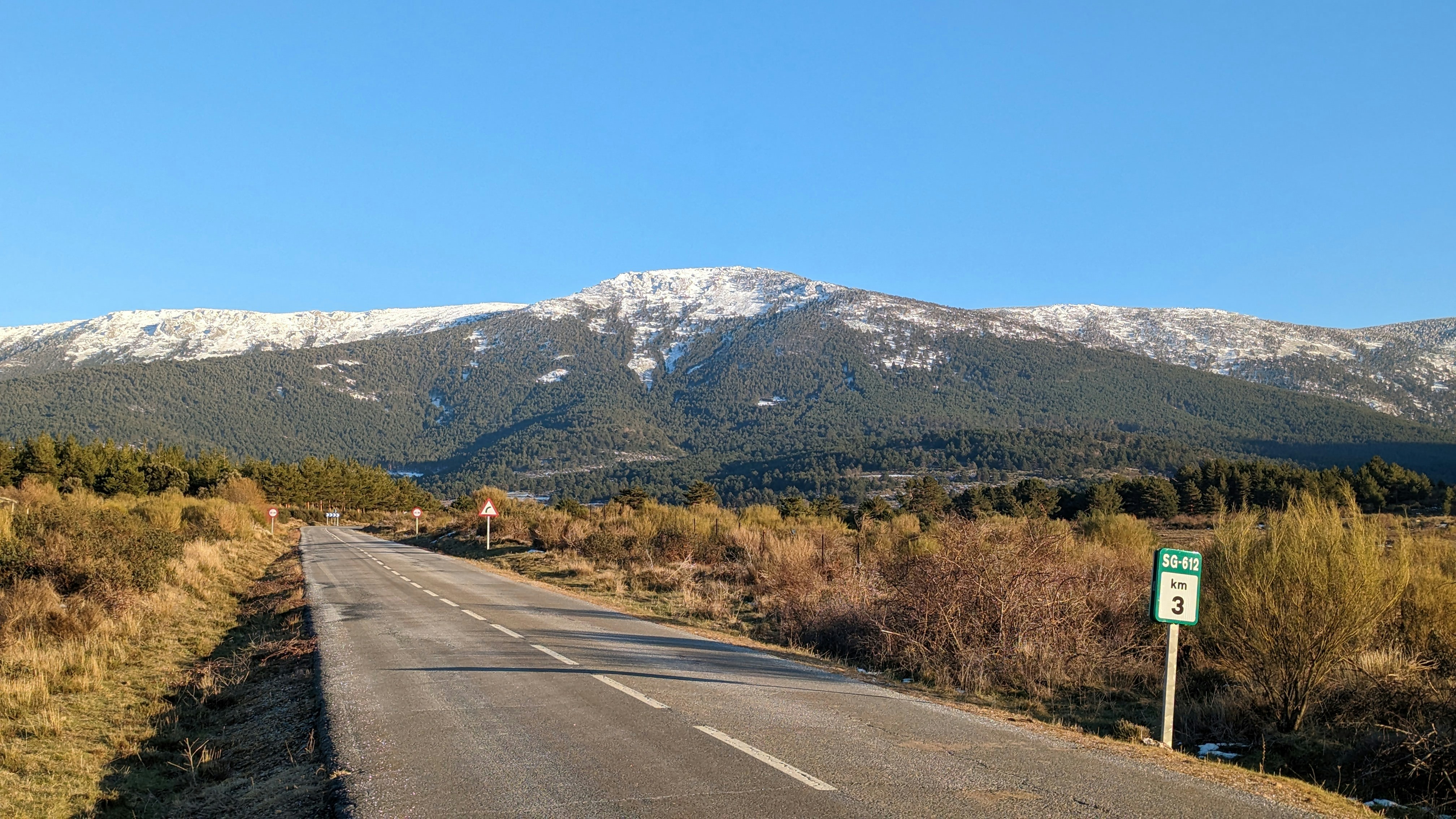 Asphalt Ribbon Toward a Snow-Kissed Alpine Ridge