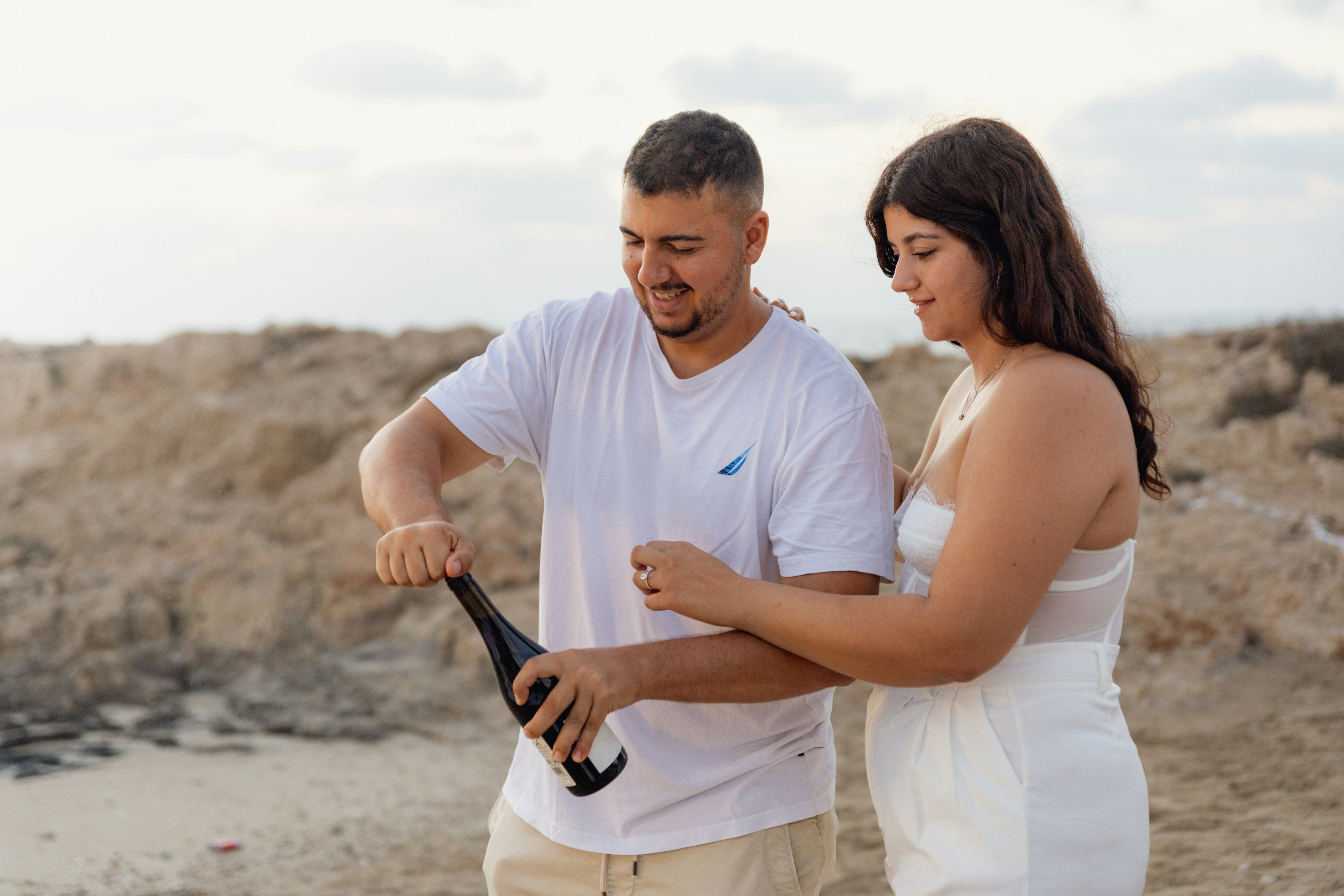 Couple opening champagne bottle on a beach
