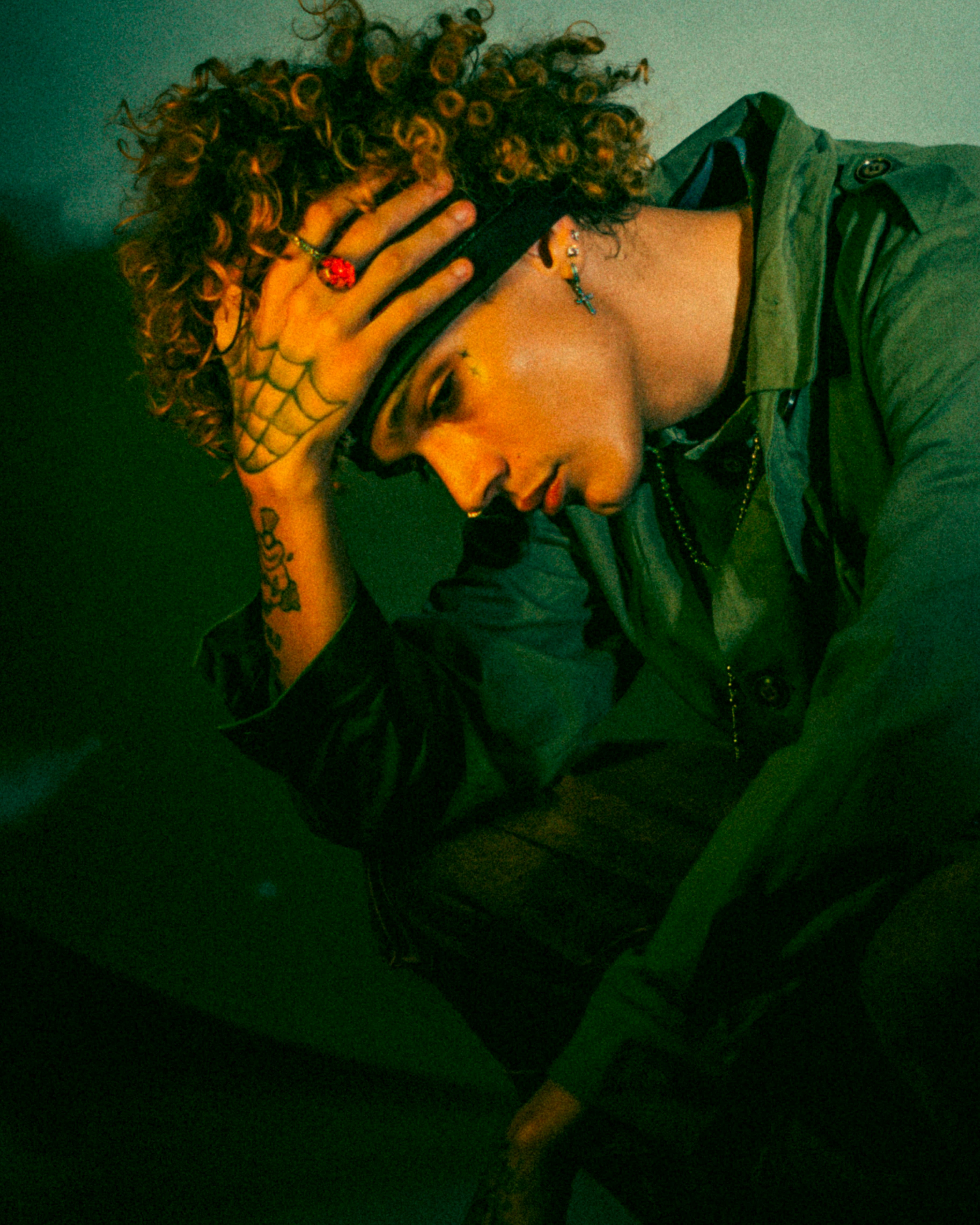 Green Hour Reverie: A Contemplative Portrait with Curly Hair and Tattooed Hand Under Moody Lighting