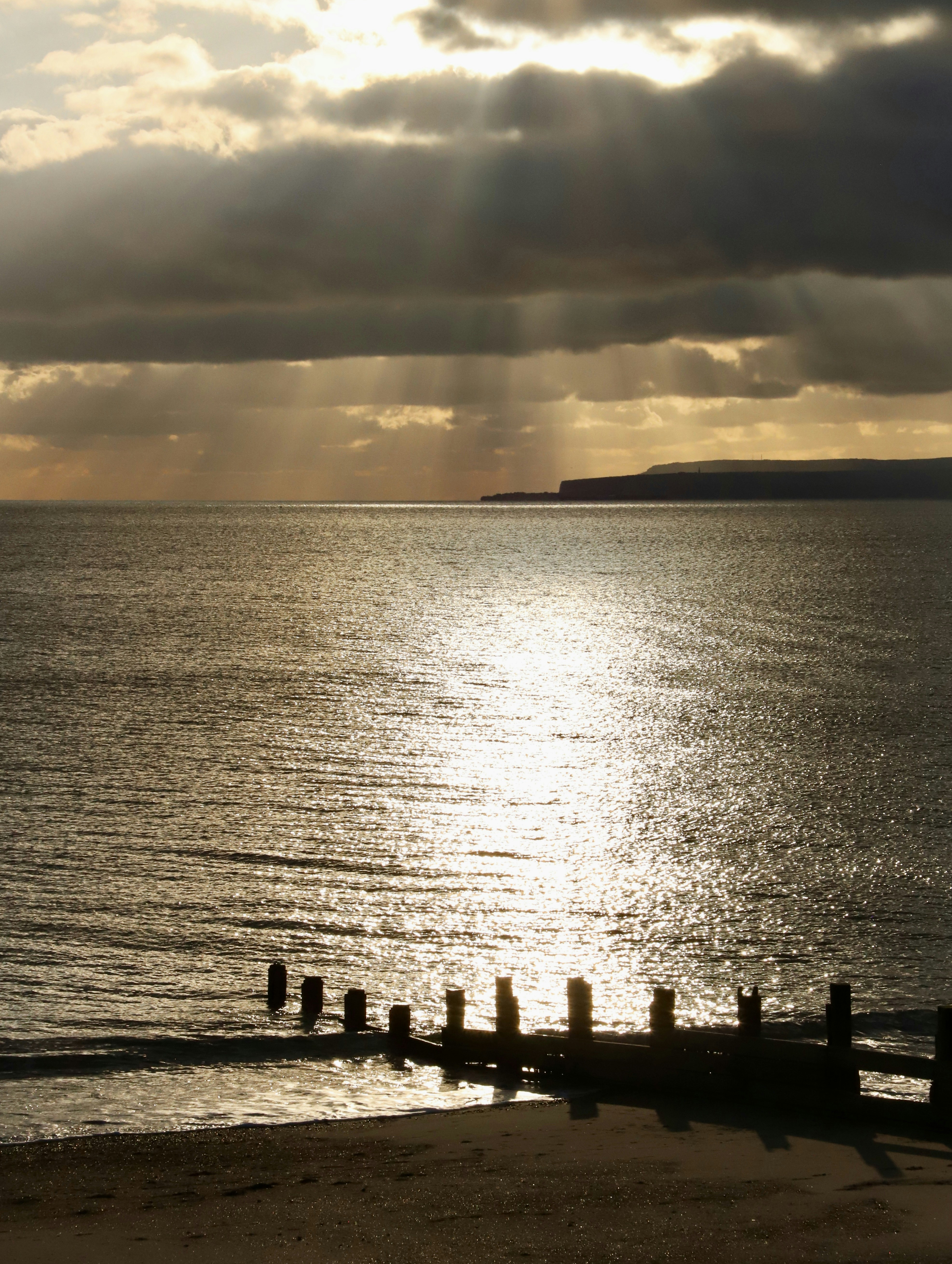 Sunbeams on the Quiet Sea: Light Through Clouds Over a Weathered Pier