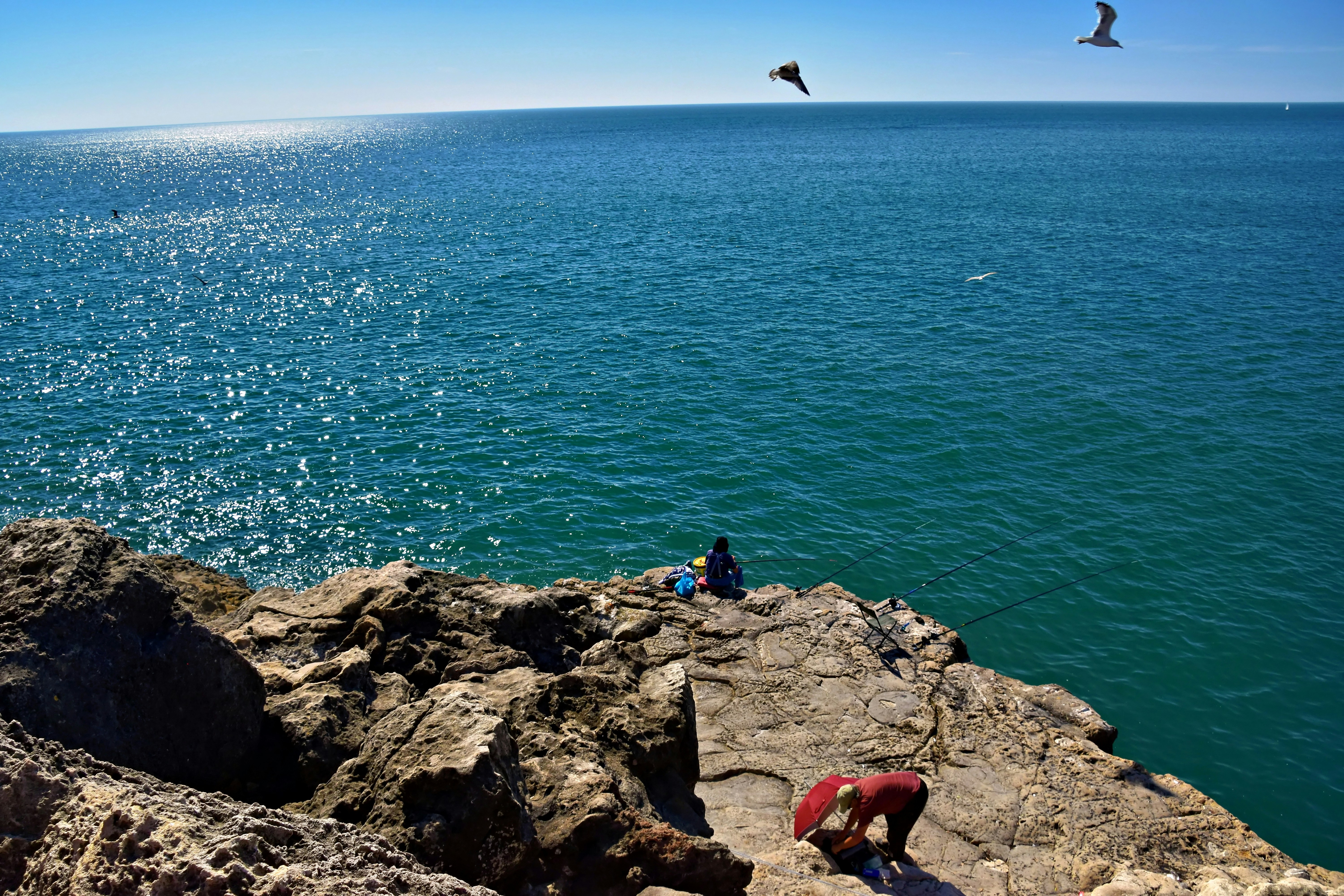 Blue-Jacket at the Edge: solitary figure on sunlit cliff above a glittering sea