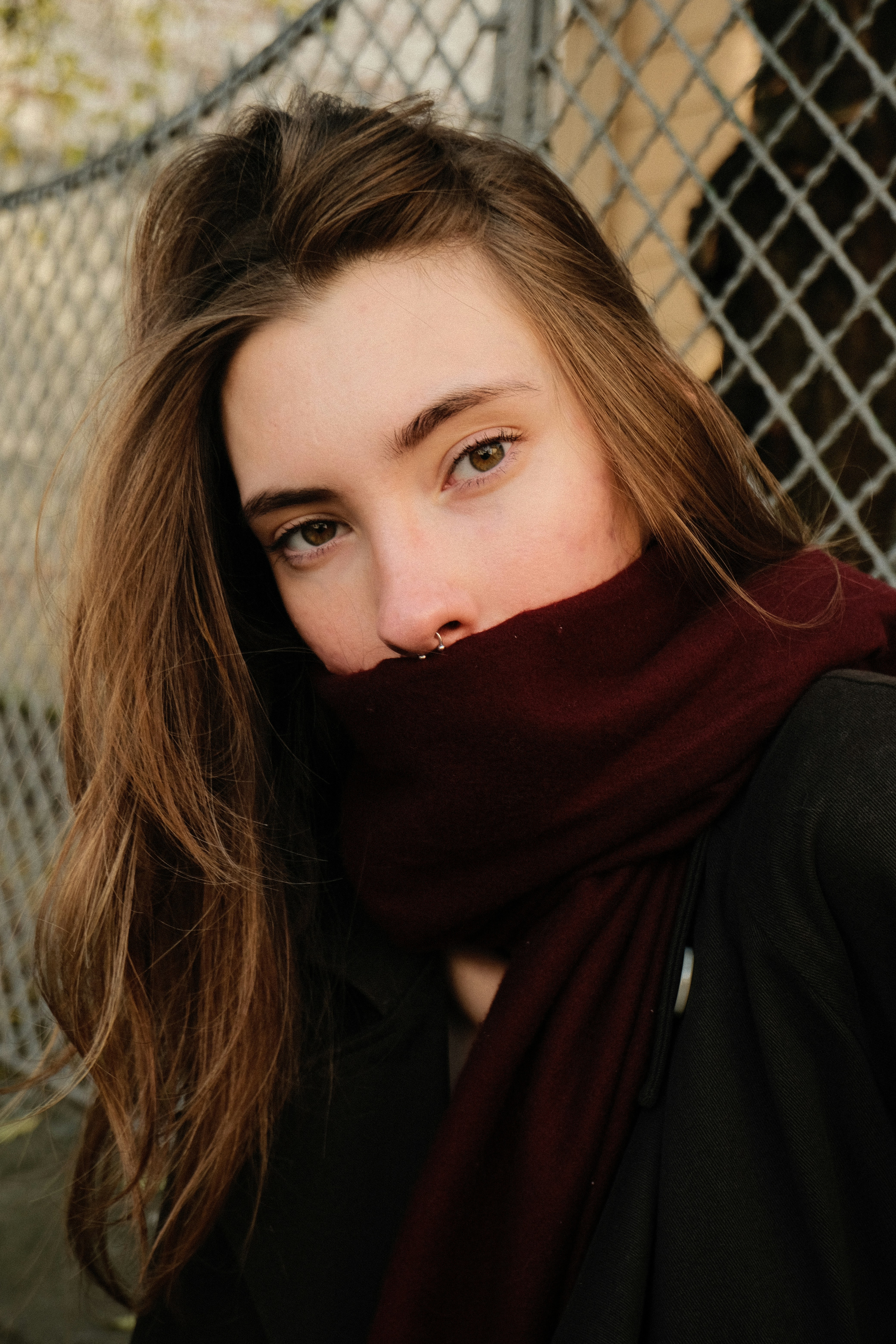 Through the Fence: A Quiet Gaze Beneath a Maroon Scarf