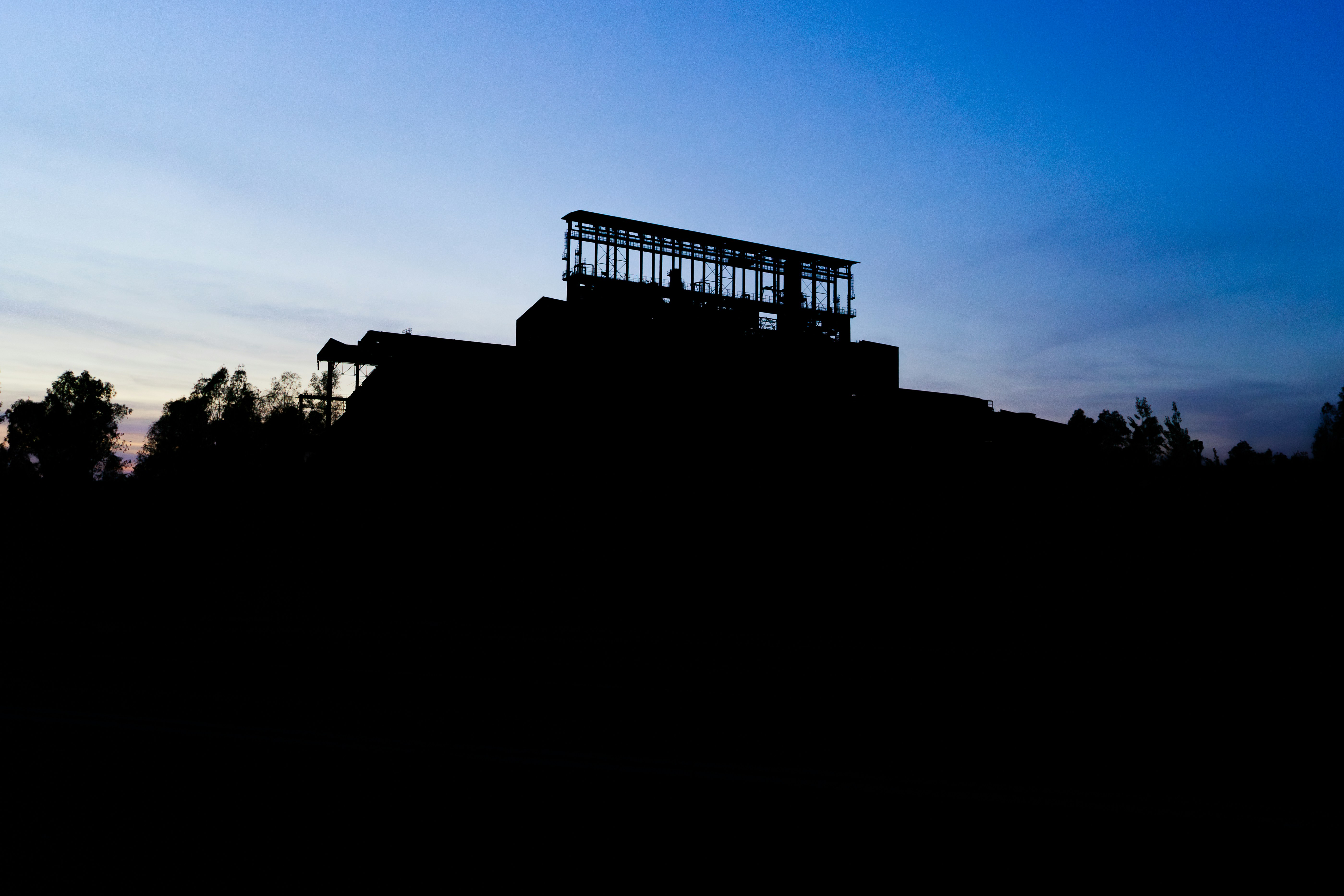 Twilight Silhouette: An Industrial Edifice Reigning Over a Quiet Hill