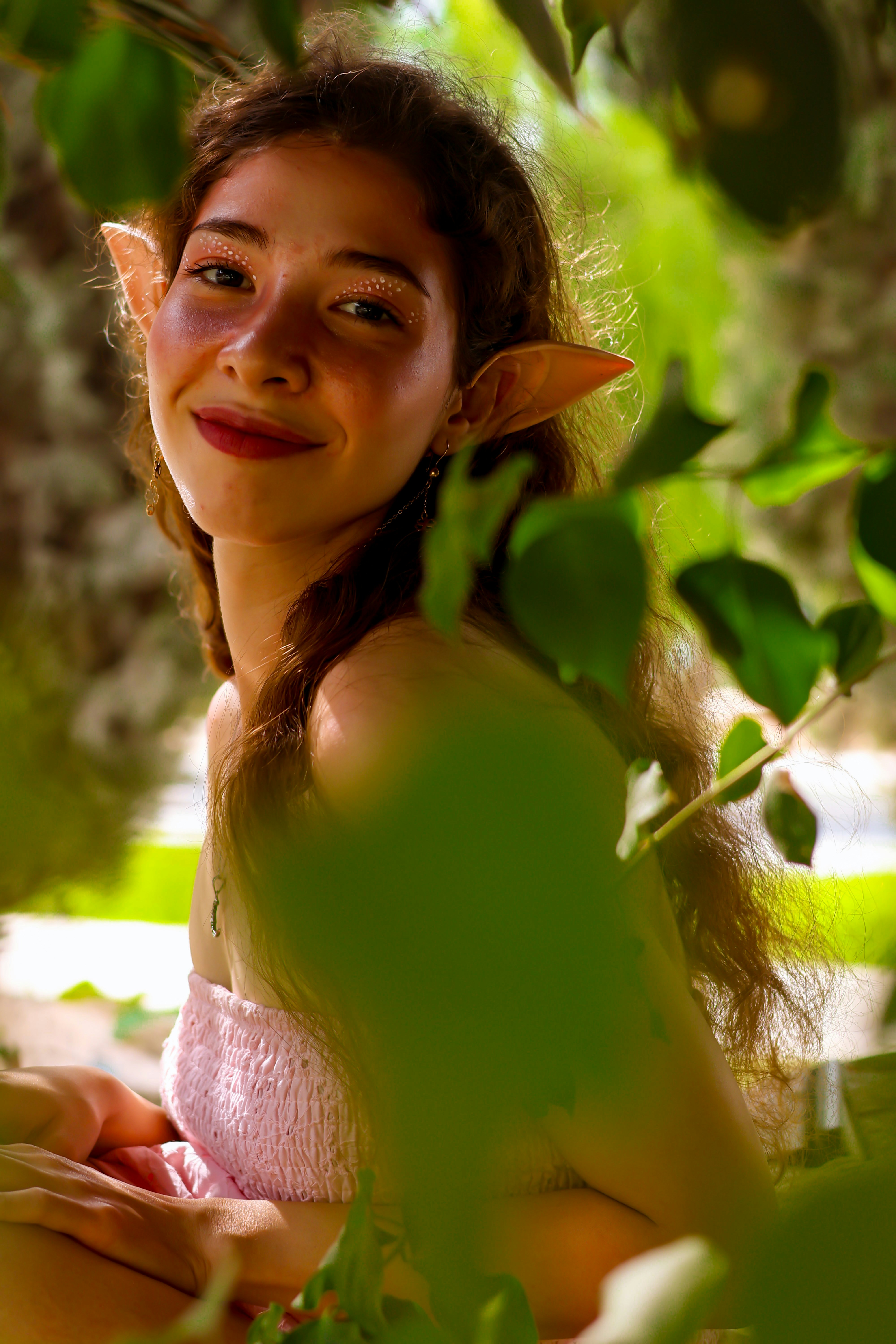 A warm, whimsical portrait featuring soft glitter makeup, elf-ear details, and vibrant garden florals. The image blends fantasy and natural beauty, creating a gentle, magical atmosphere.