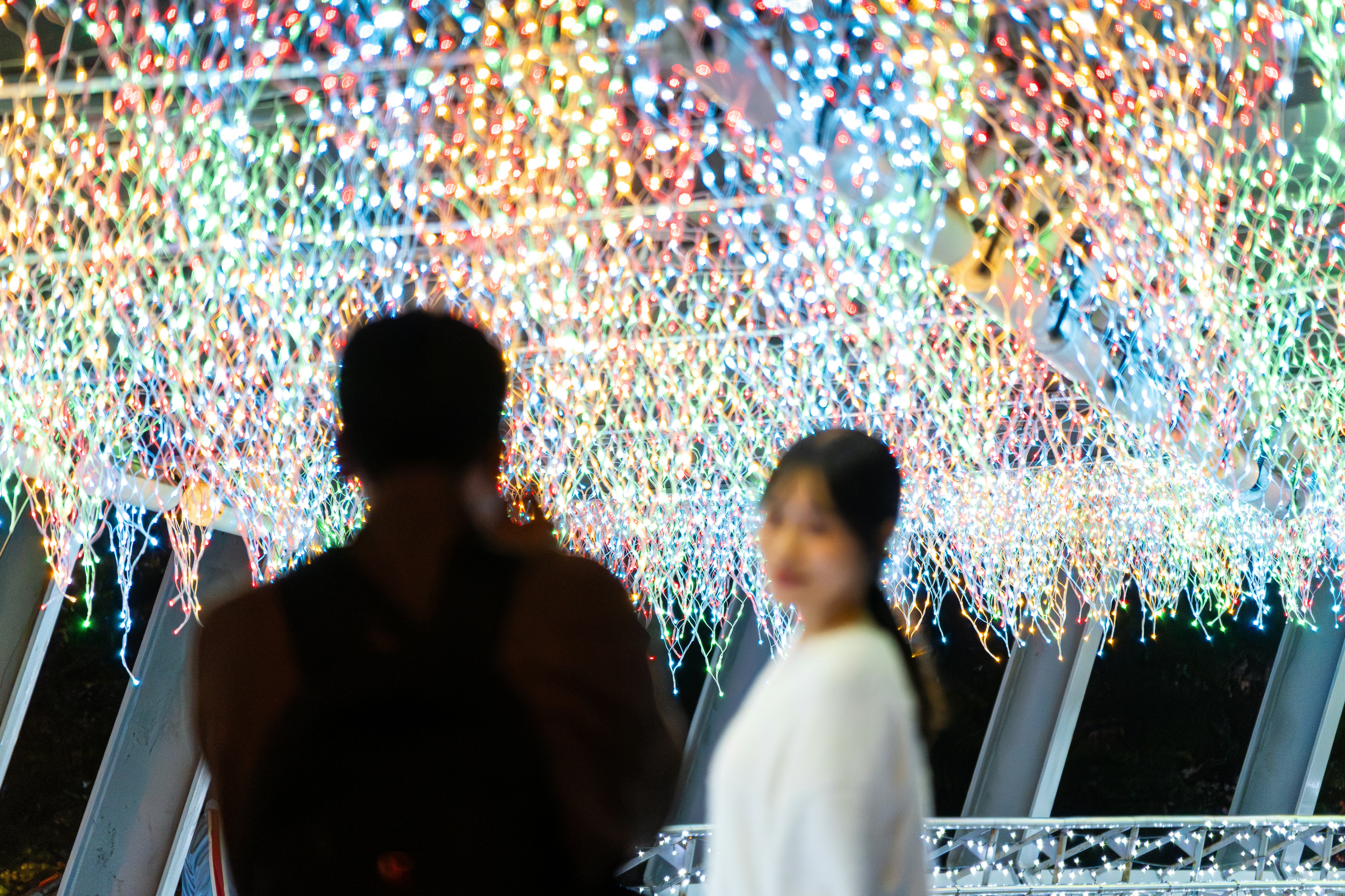 Canopy of Colorful Orbs: Silhouettes Beneath a Night Atrium