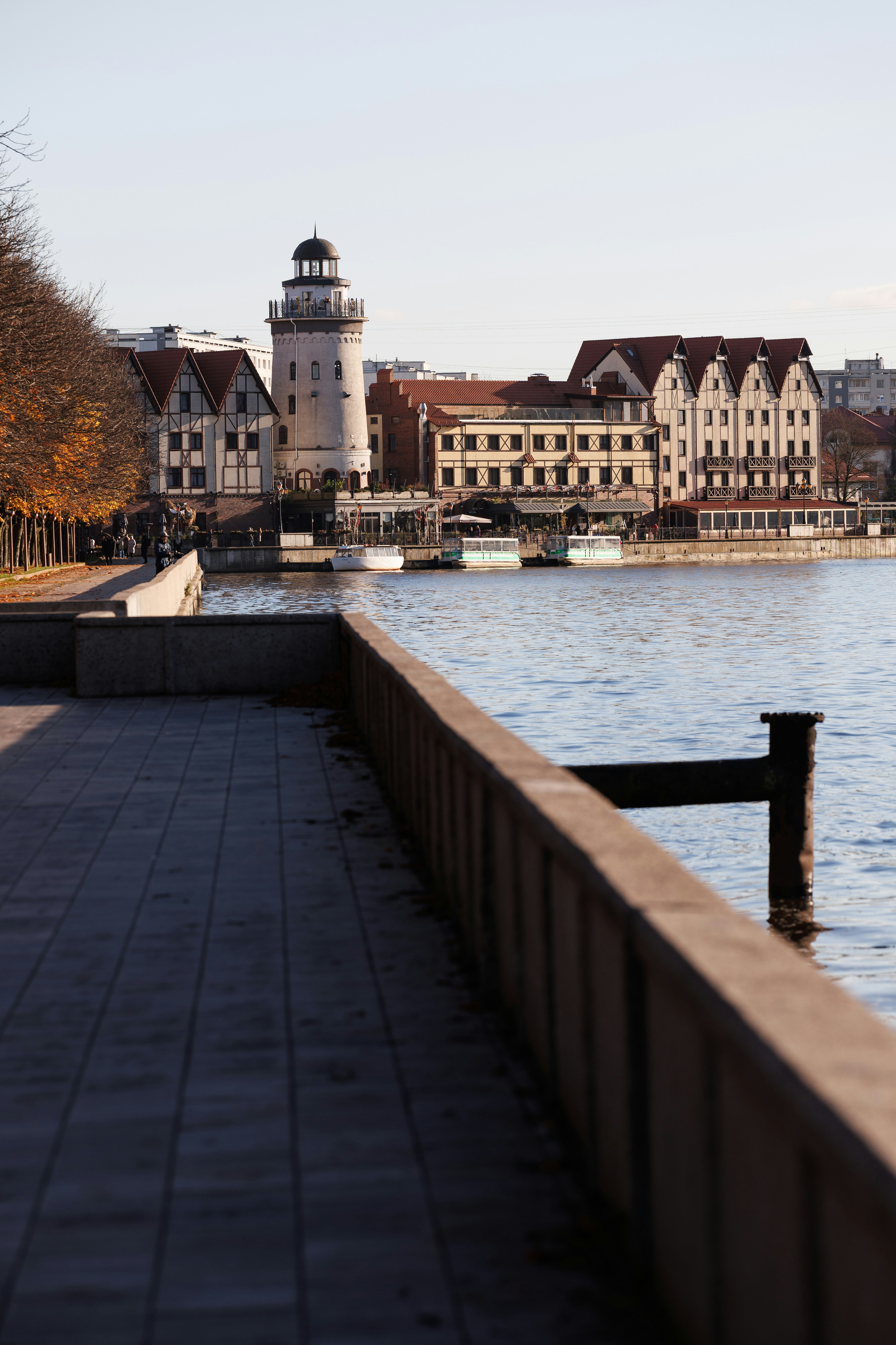Historic lighthouse and waterfront promenade with autumn trees along the river in Kaliningrad