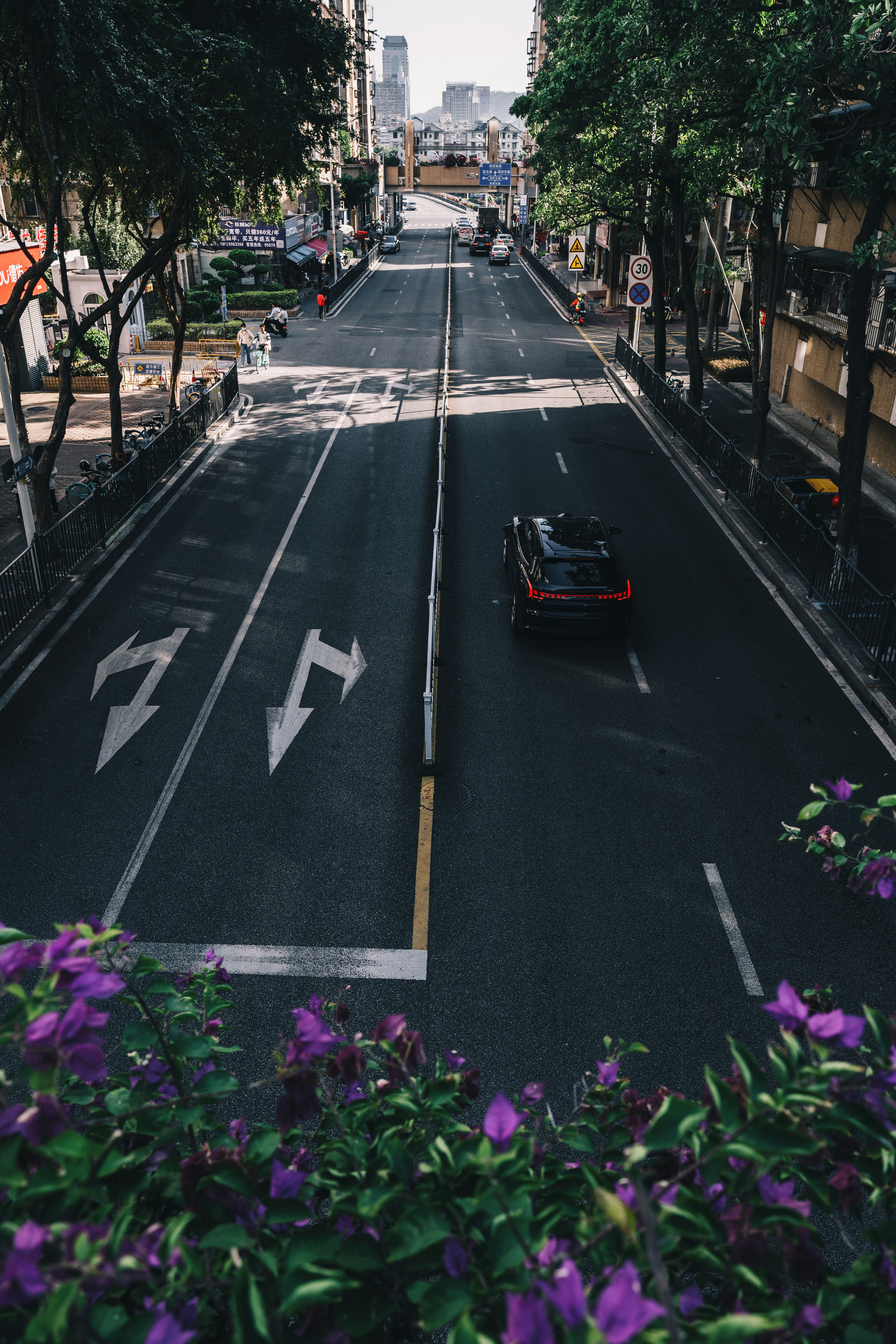 Aisle of Asphalt: a lone car threads a sunlit boulevard through a canyon of city balconies