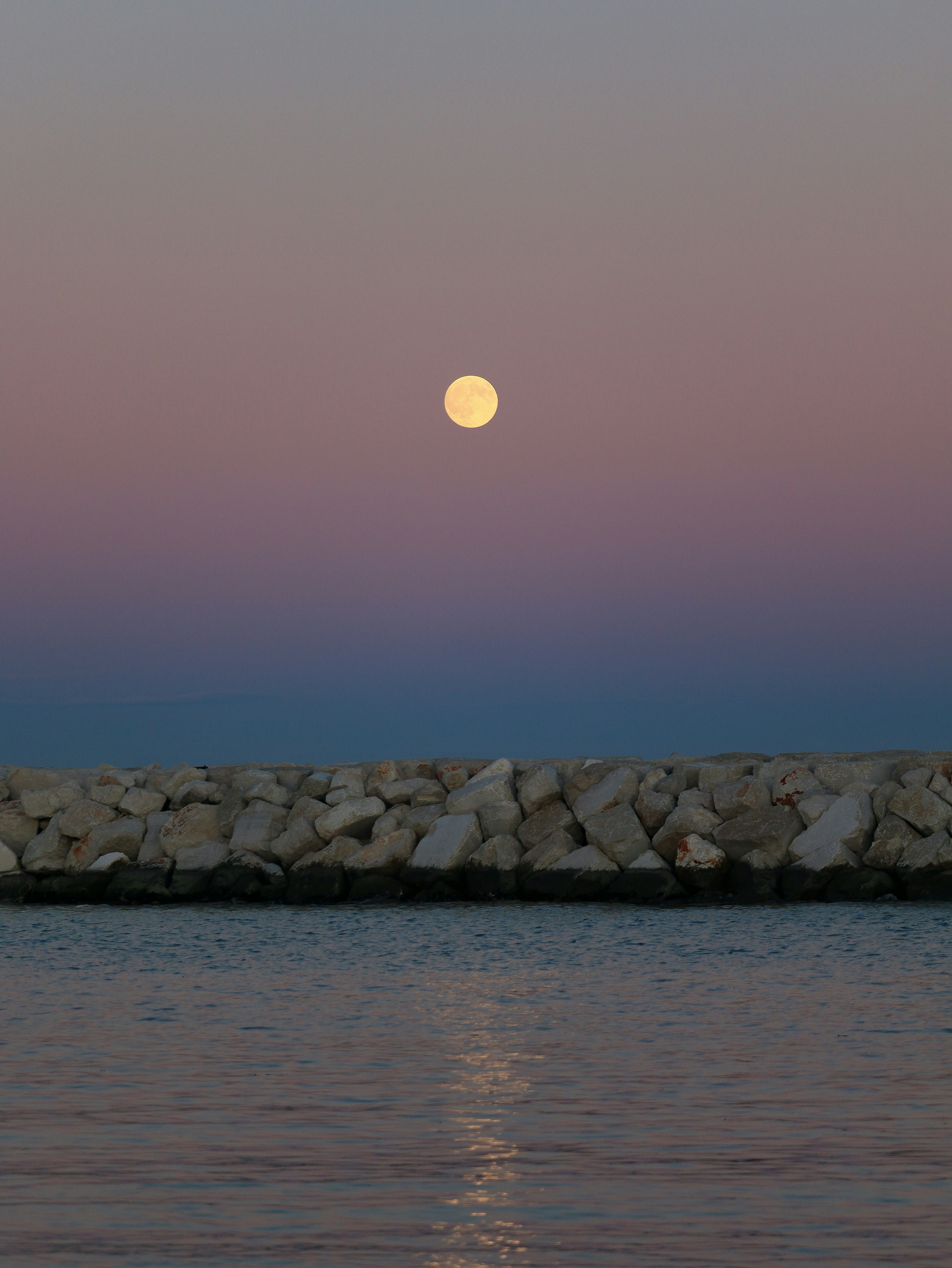 Luna Over the Breakwater: Twilight Moonrise Reflects on Quiet Seas